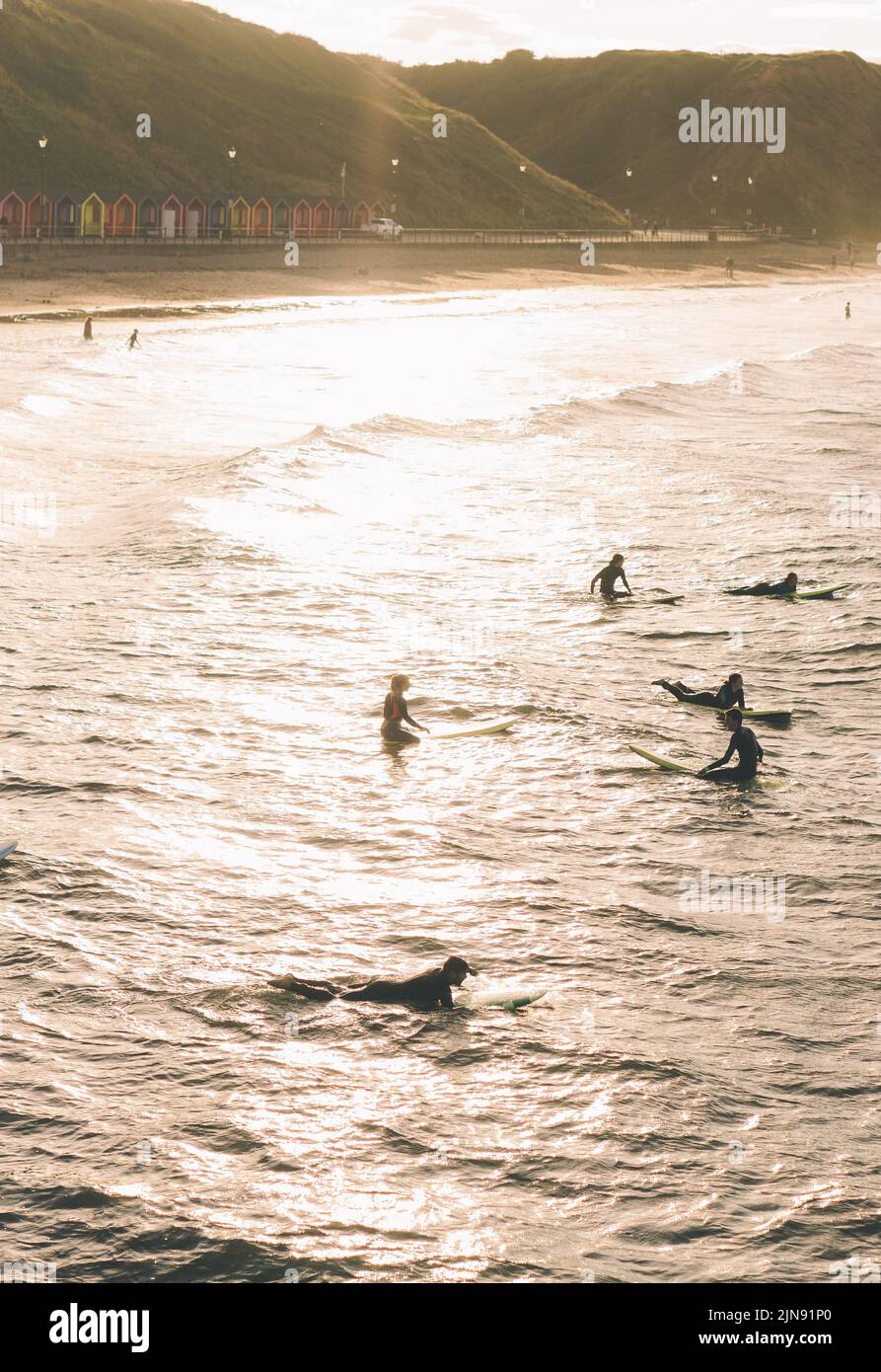 A vertical shot of young people surfing on sea waves at golden hour in ...