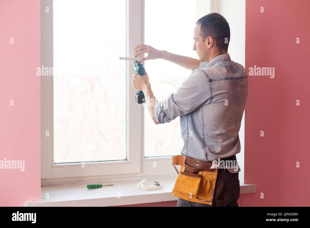Handyman using a cordless screwdriver to install a window handle ...