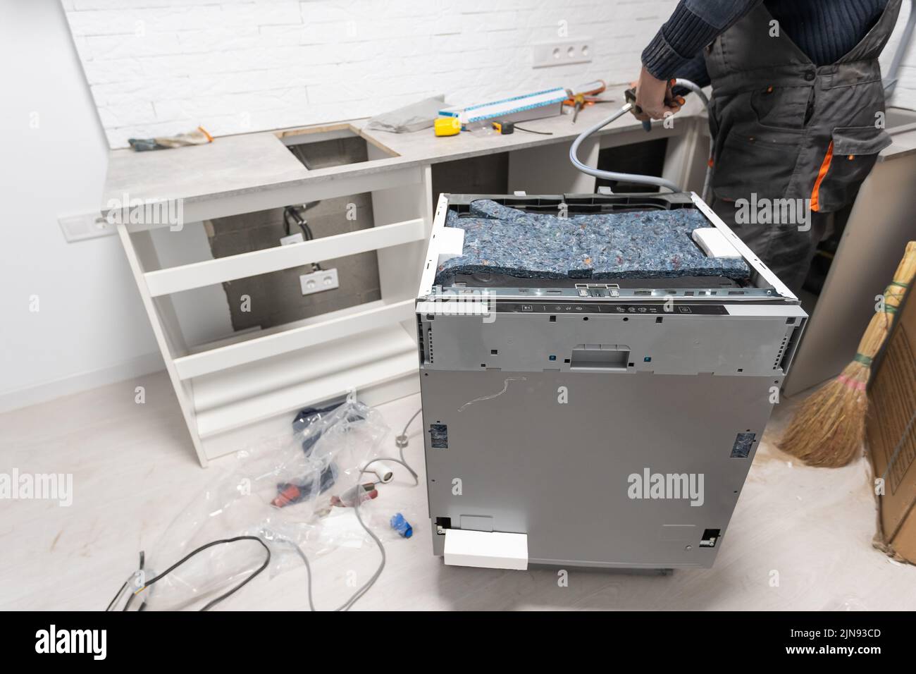 Appliance technician working under a kitchen sink installing a ...