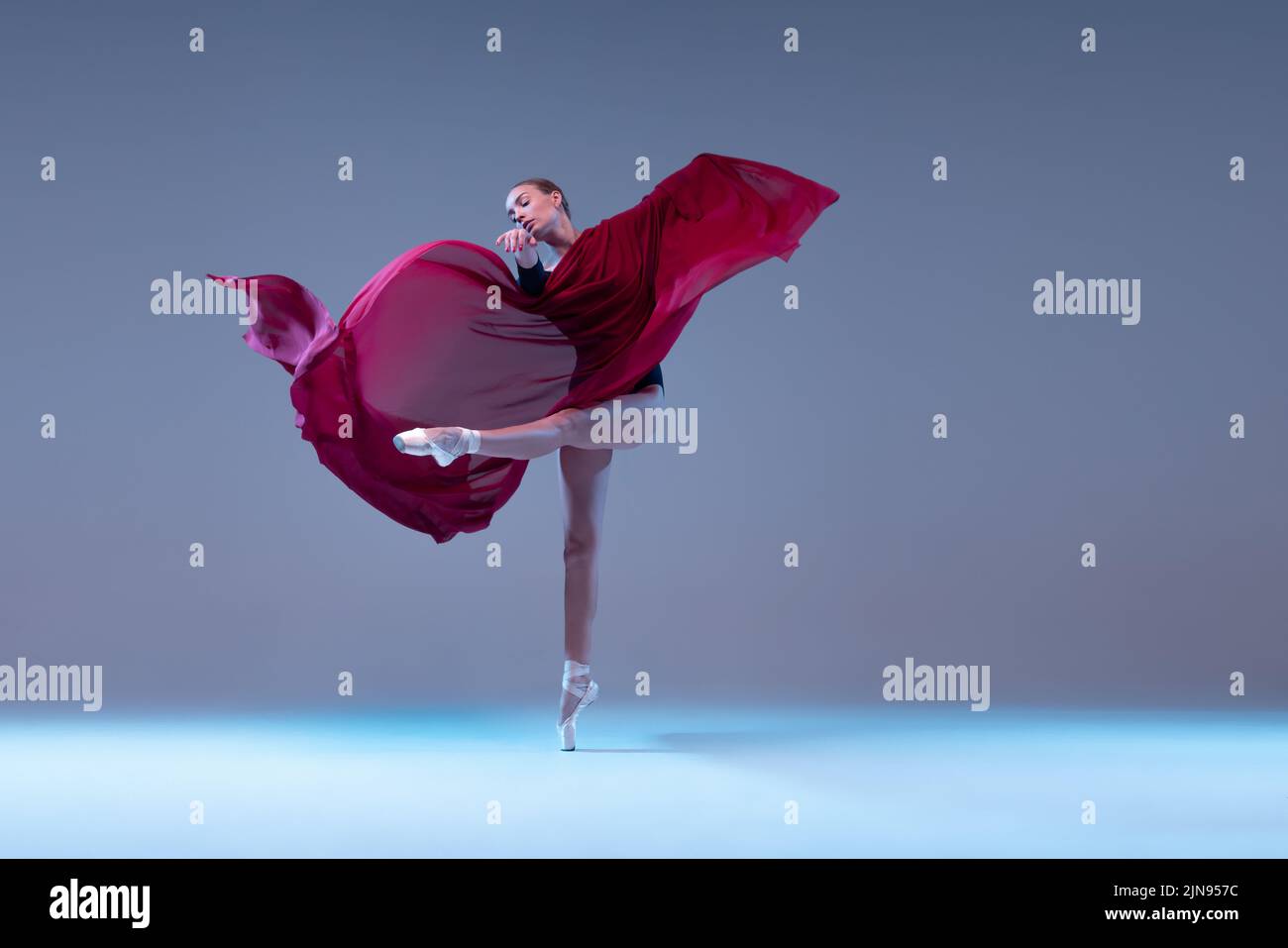 Portrait of young ballerina dancing with fabric isolated over blue grey ...