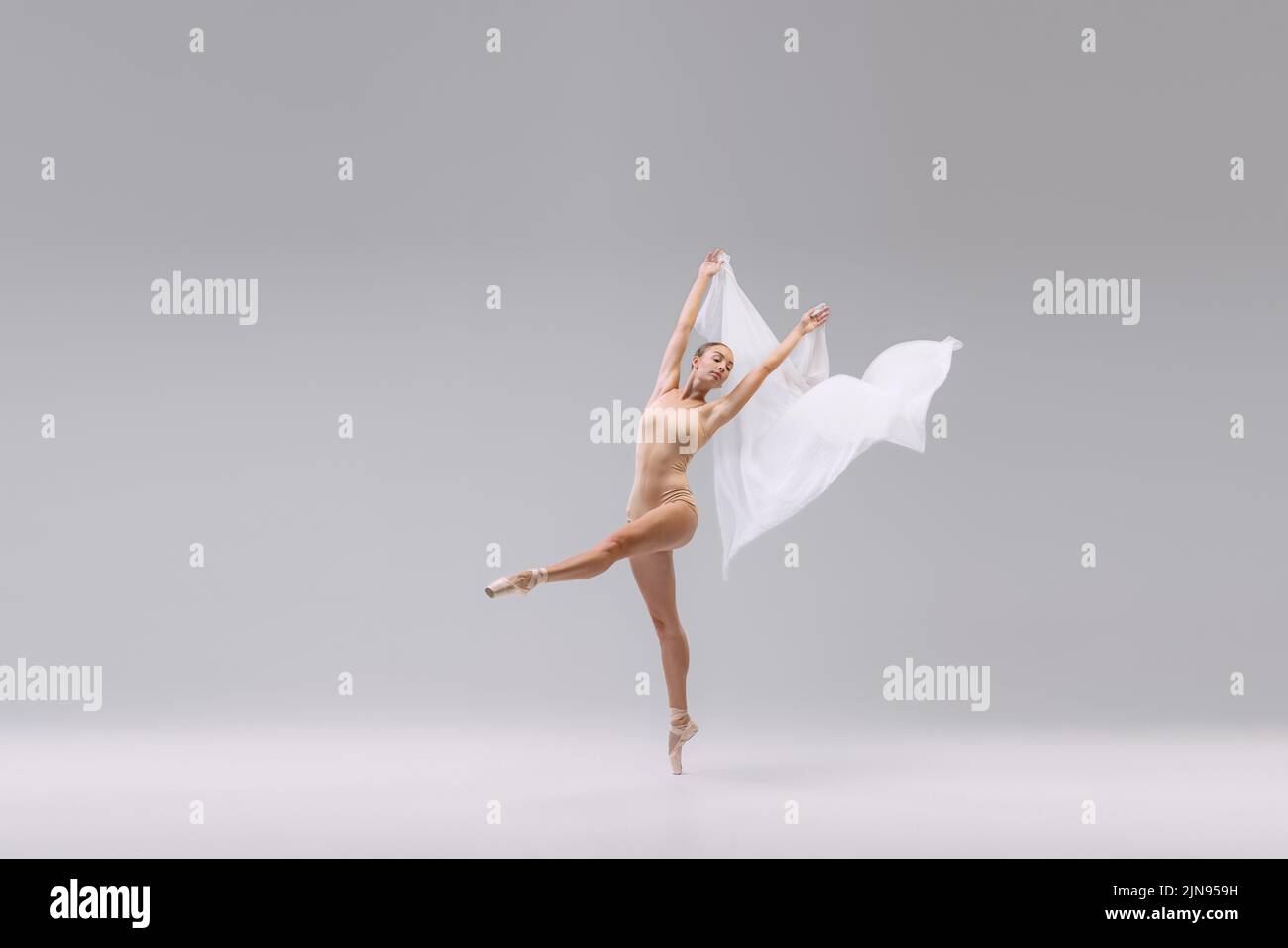 Portrait of young ballerina dancing with fabric isolated over grey studio background. Grace ...