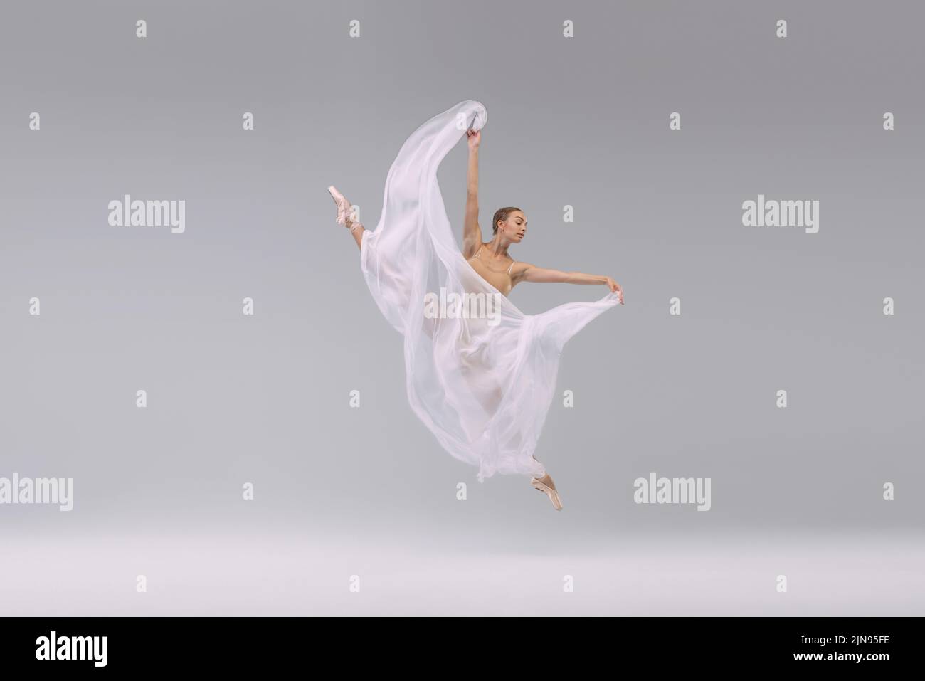 Portrait of young beautiful ballerina dancing, jumping with transparent fabric isolated over ...