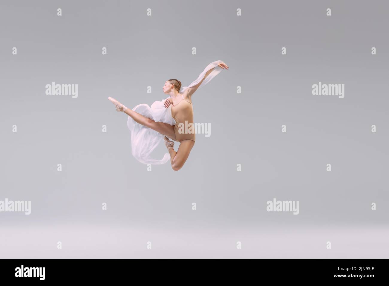 Portrait of young ballerina dancing with fabric isolated over grey ...