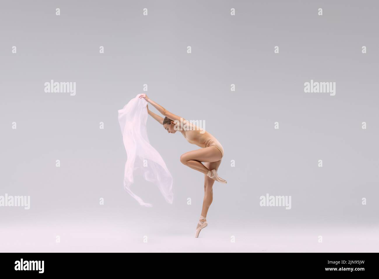 Portrait of young ballerina dancing with fabric isolated over grey ...