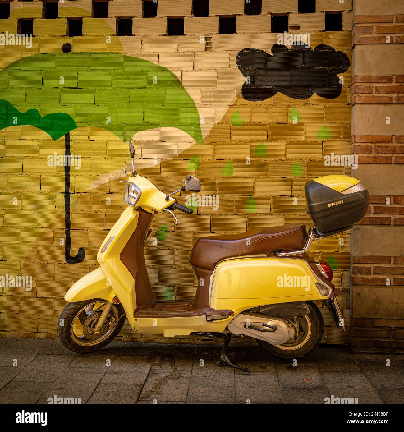 Bright yellow moped against a colourful brick wall Stock Photo - Alamy