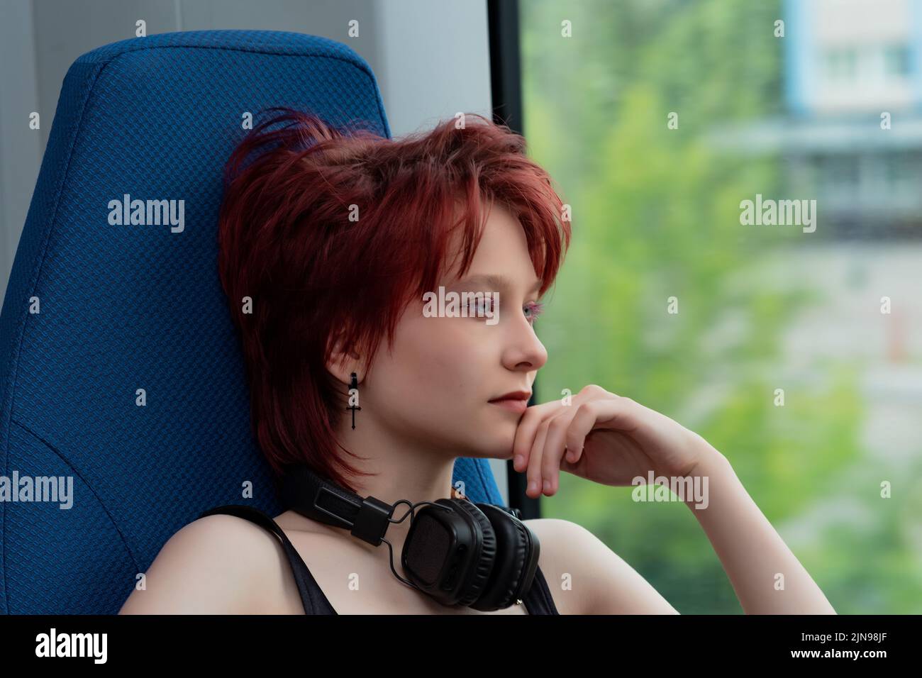 young woman with headphones rides in a moving suburban train and looks ...