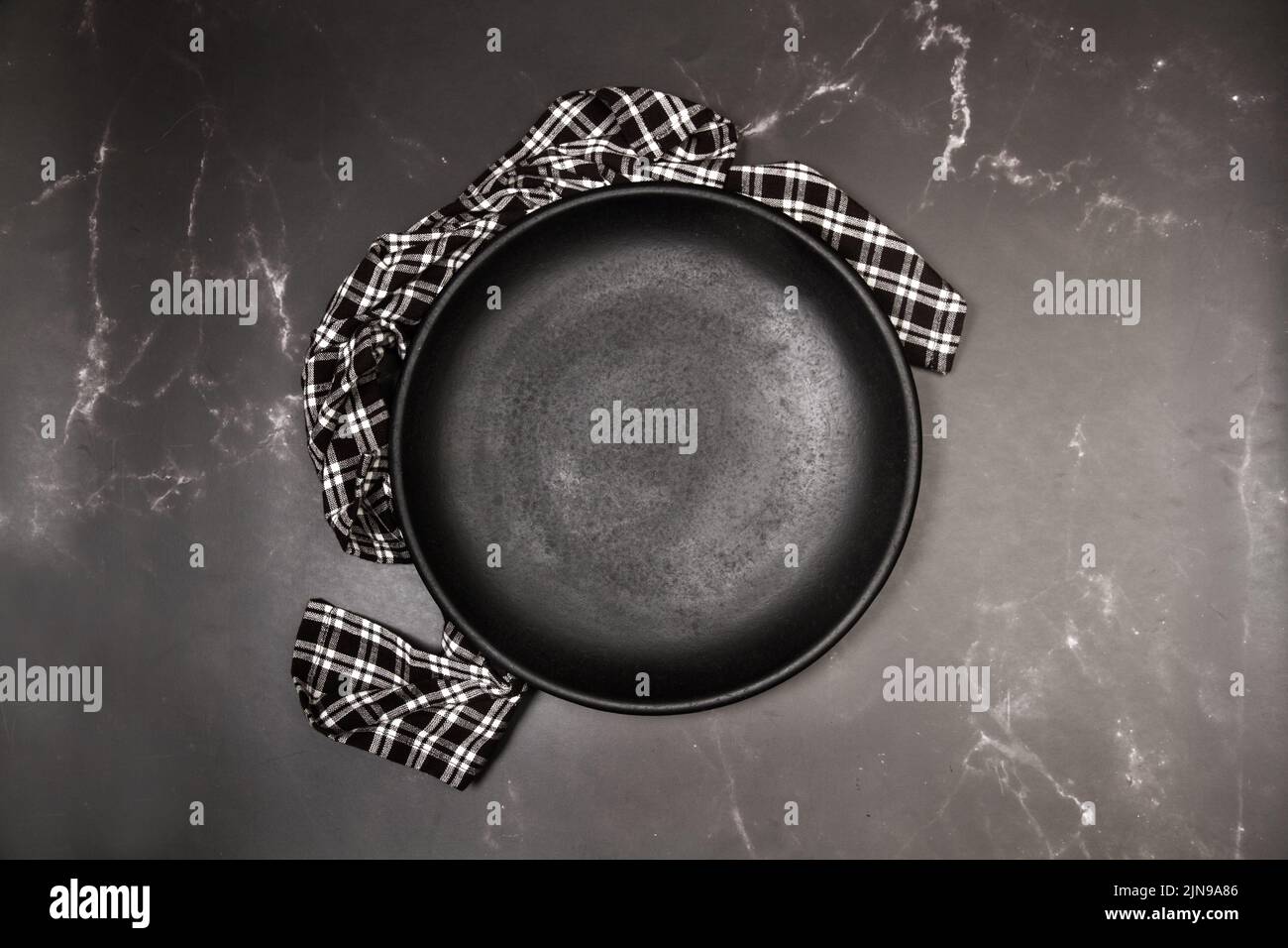 Black round flat plate on a black marble kitchen counter in a top view ...