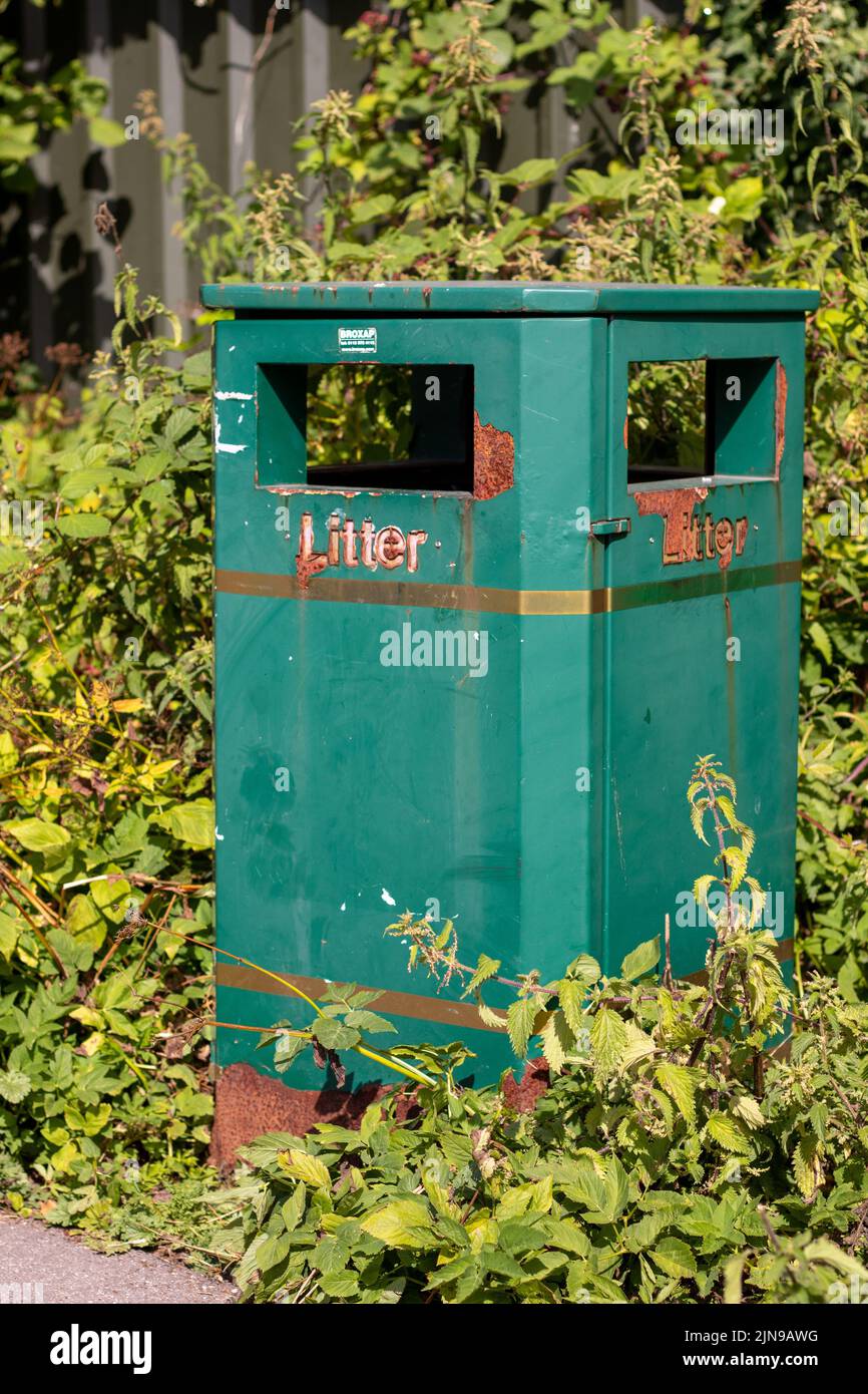 Photo of a litter bin. The bin is rusty and is surrounded by weeds ...