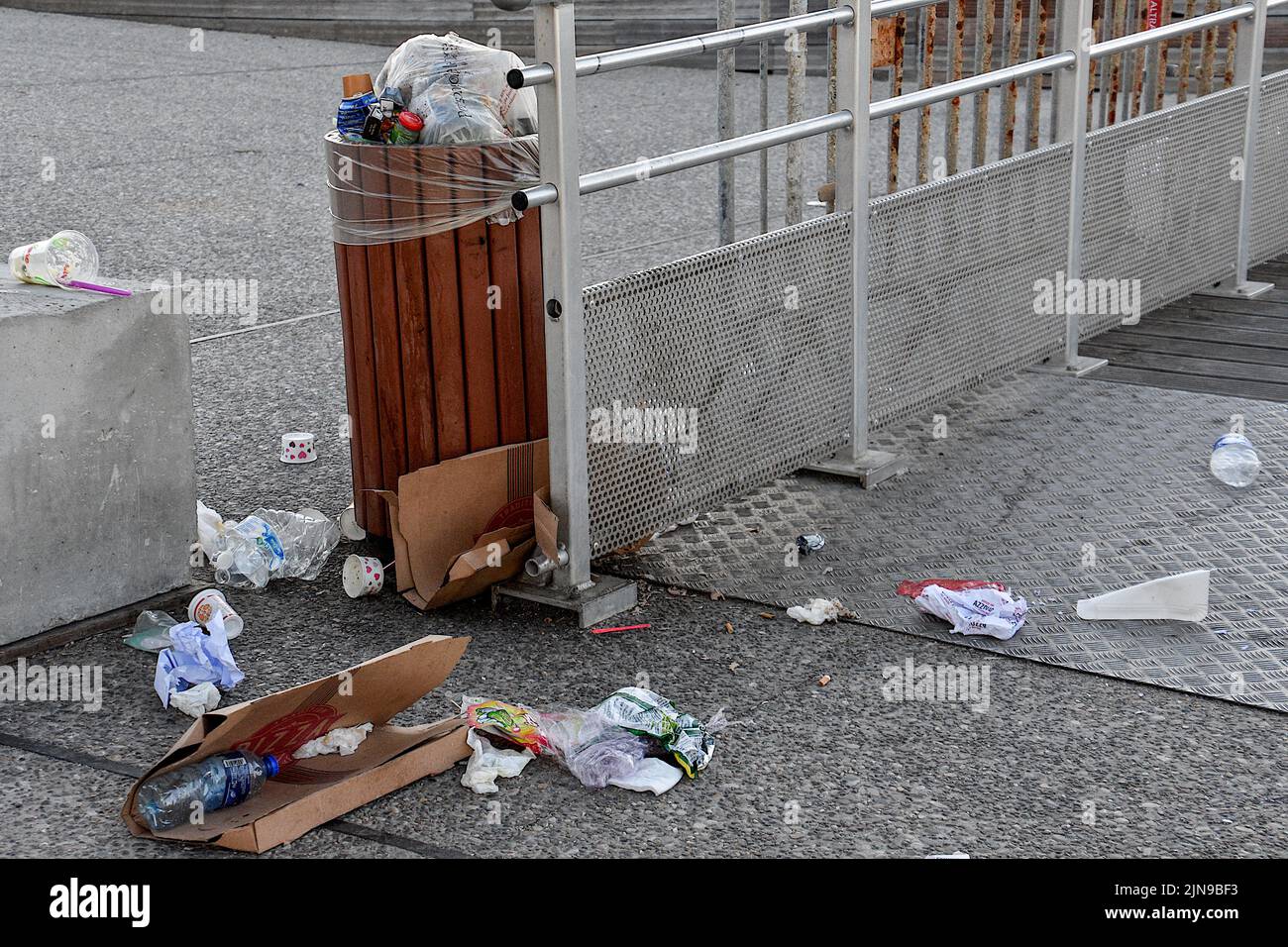 Garbage is strewn on the ground next to a full trashcan at Mistral Park ...