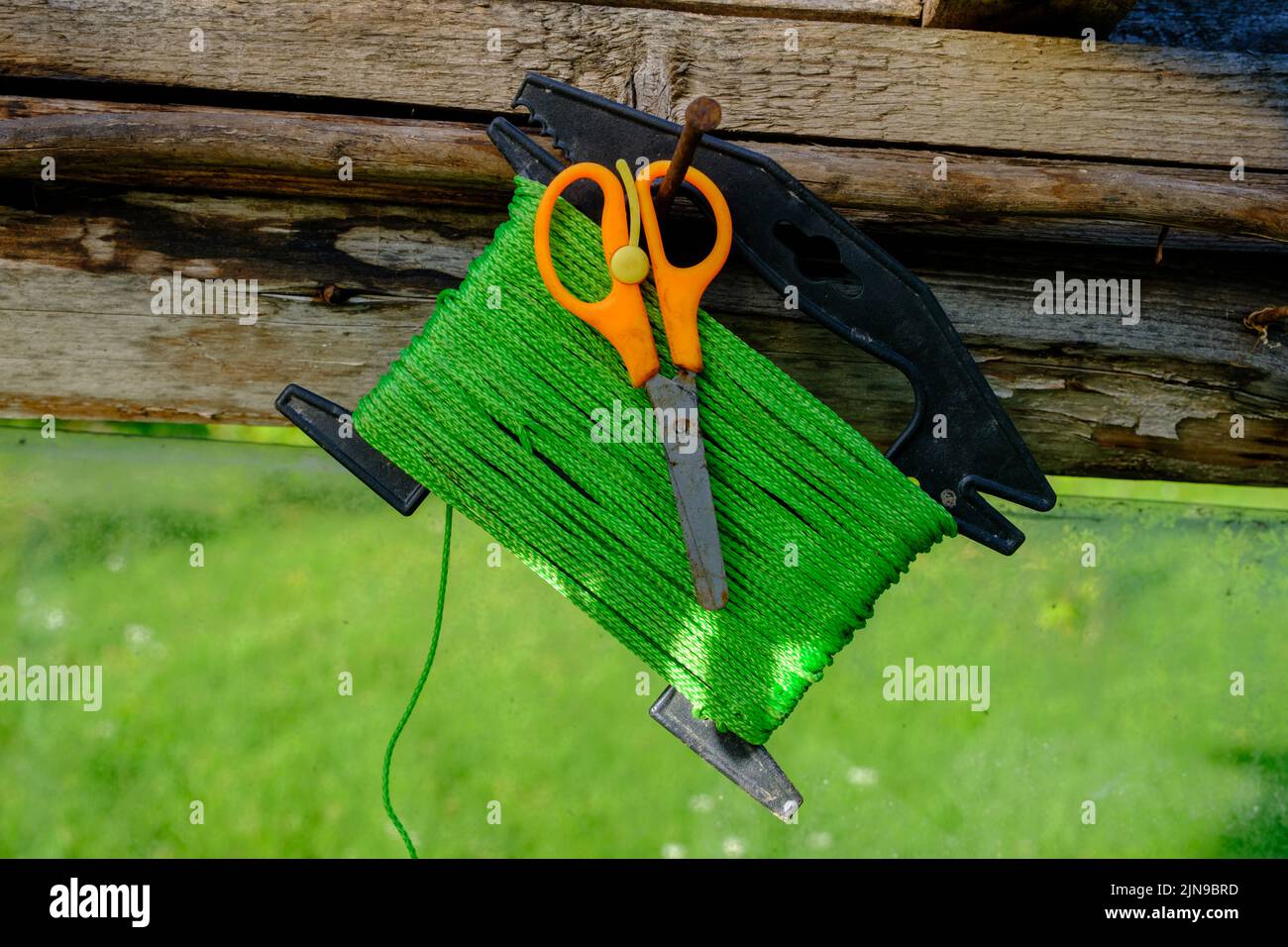 Green garden string on a spool and scissors with orange handles hung on ...