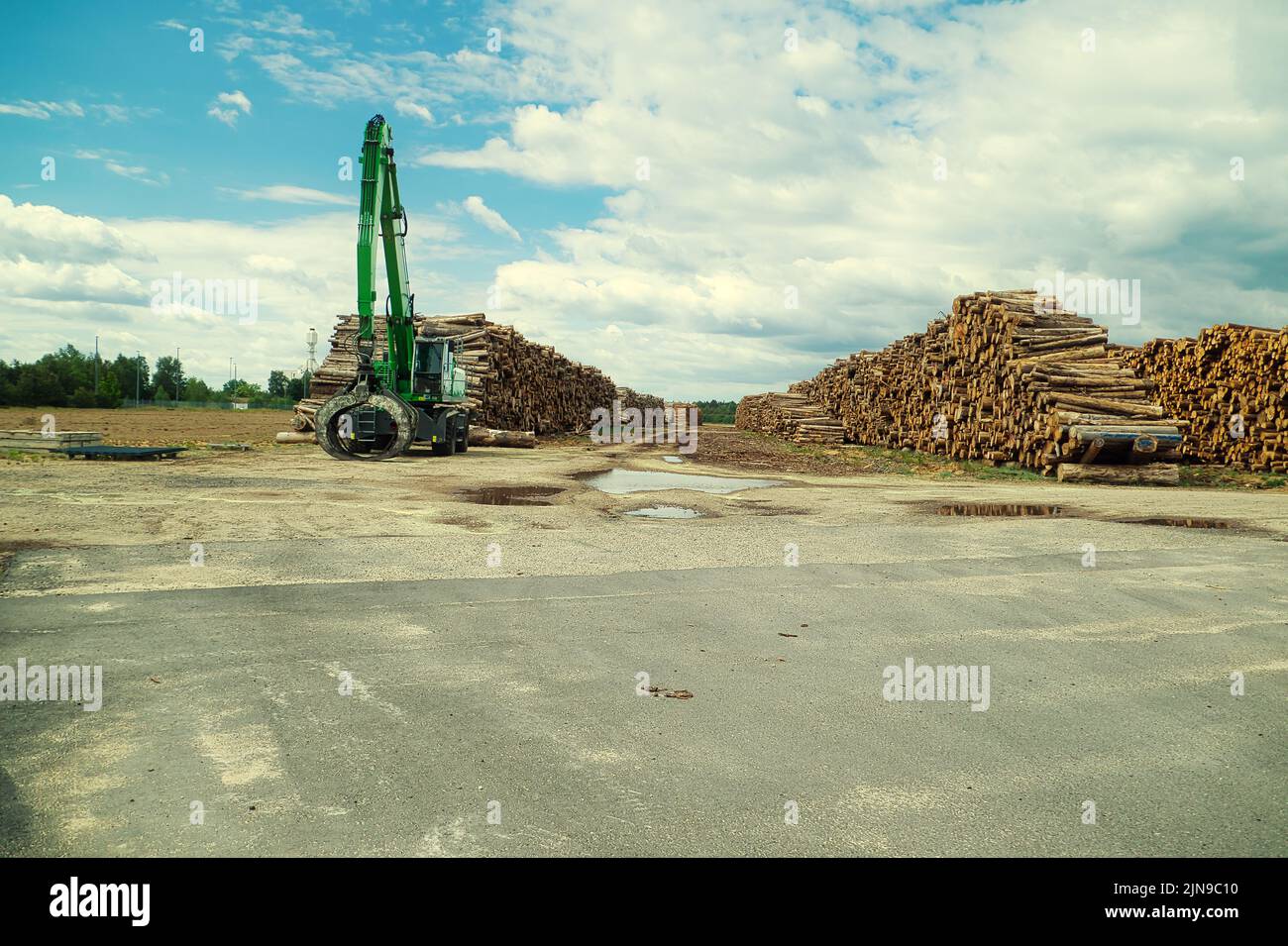 A view of old green log handling machine in background of pile of logs ...