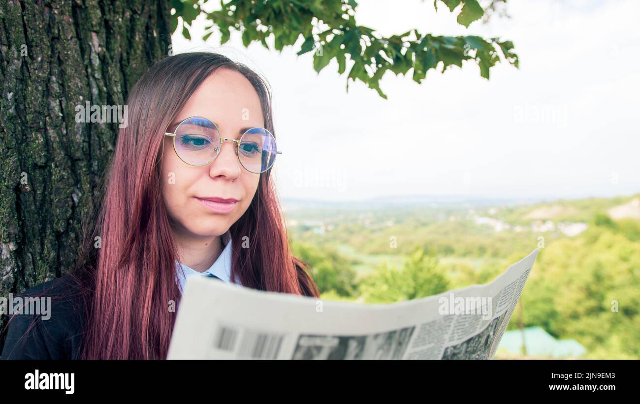 Concentrated elegant lady reading newspaper in park. Focused young ...