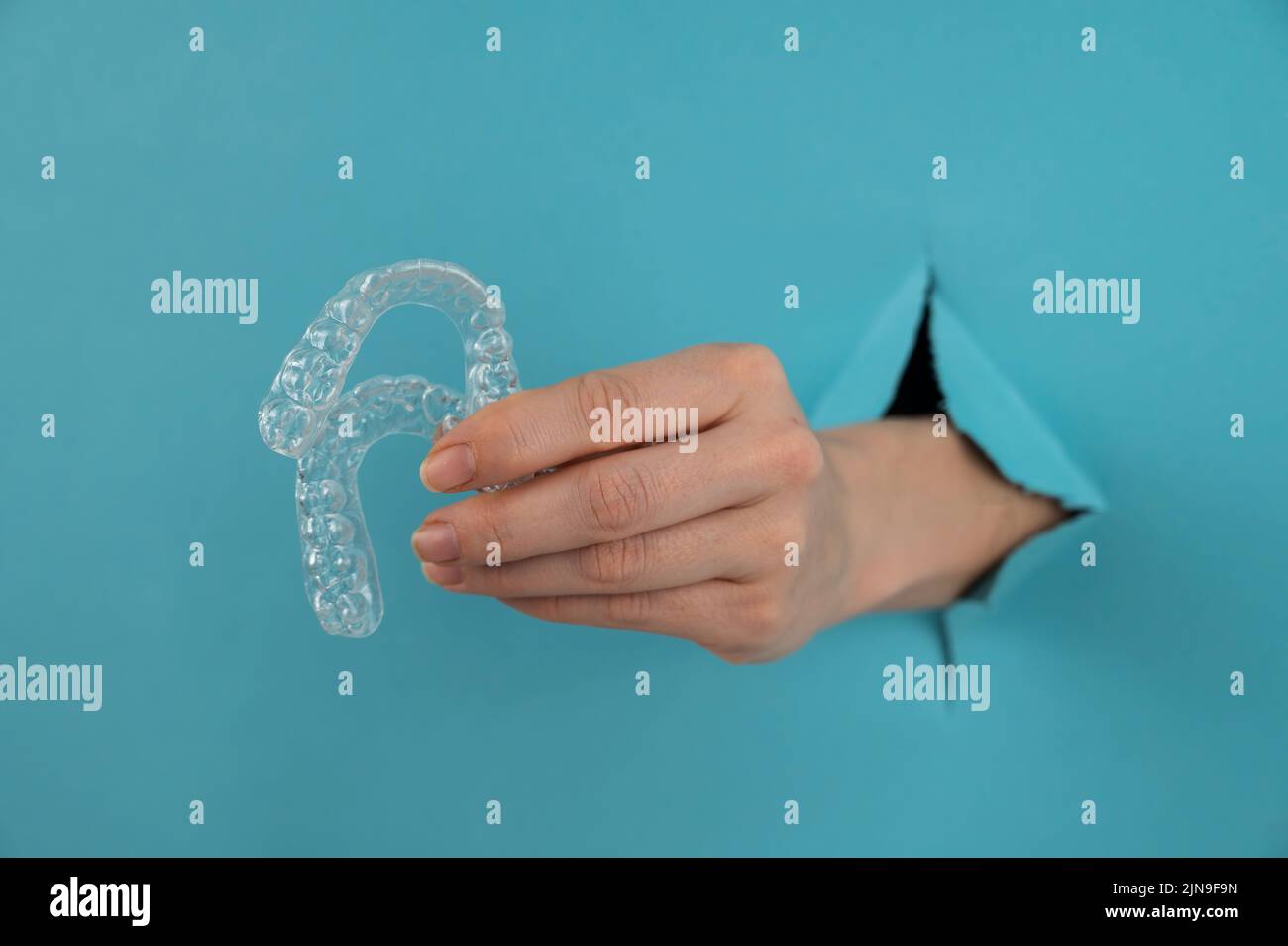 A female hand sticking out of a hole from a blue background holds ...