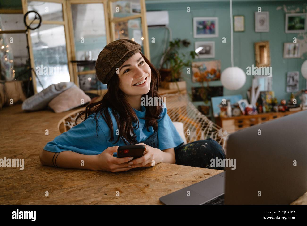 Young woman artist using gadgets while resting at her studio indoors ...