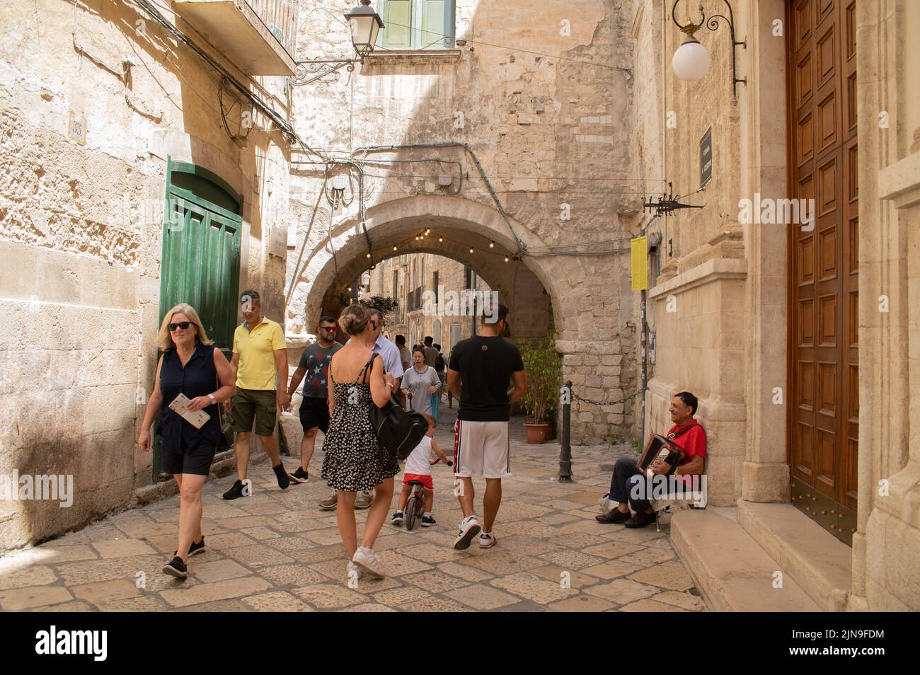 tourists in Bari old town in summer and old street musician playing the ...