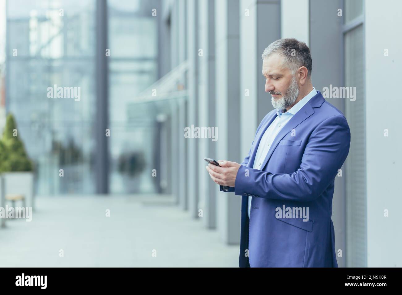 Serious and confident gray-haired man standing outside office building ...
