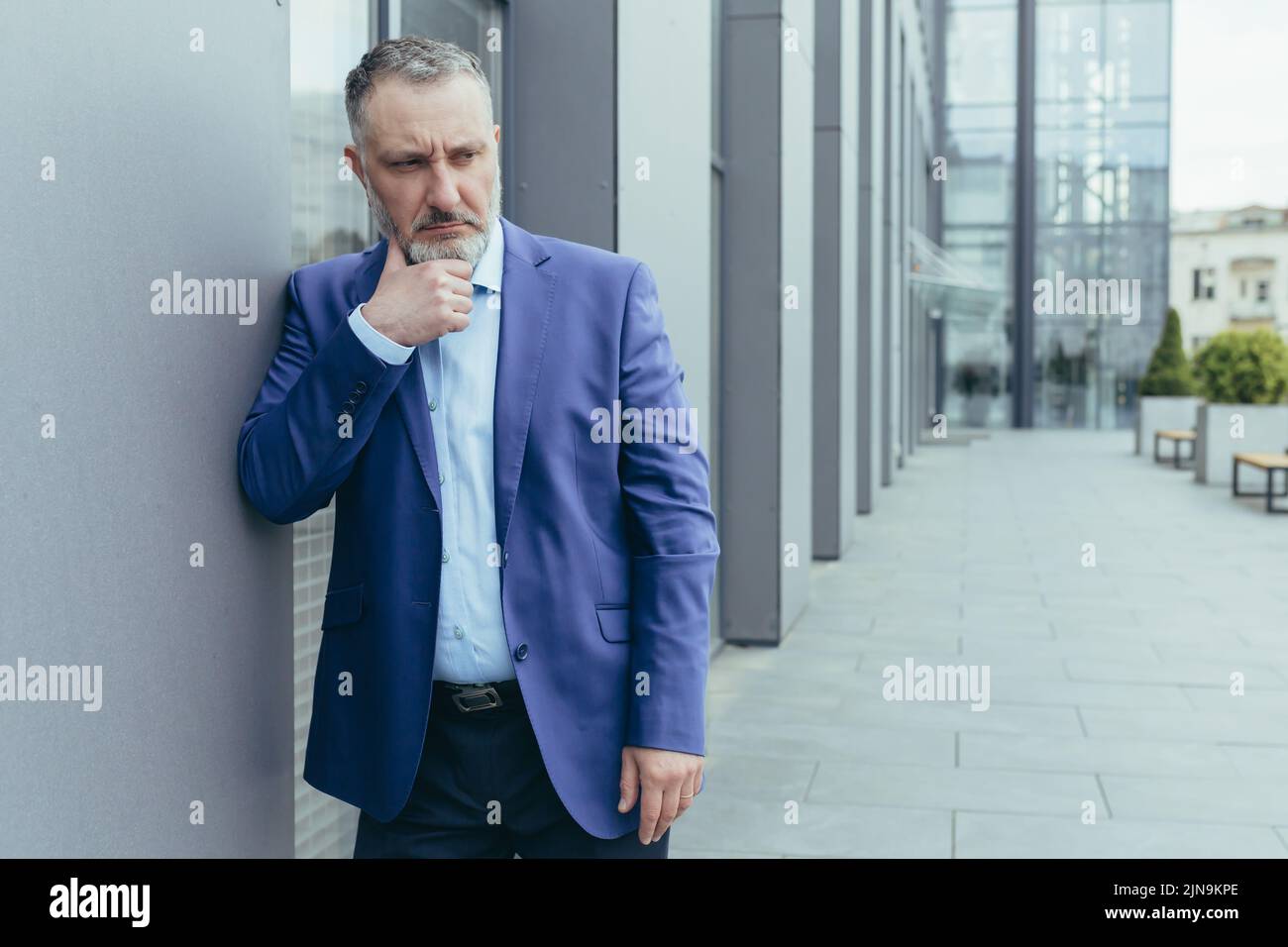 Senior gray haired man outside office building, standing and thinking ...