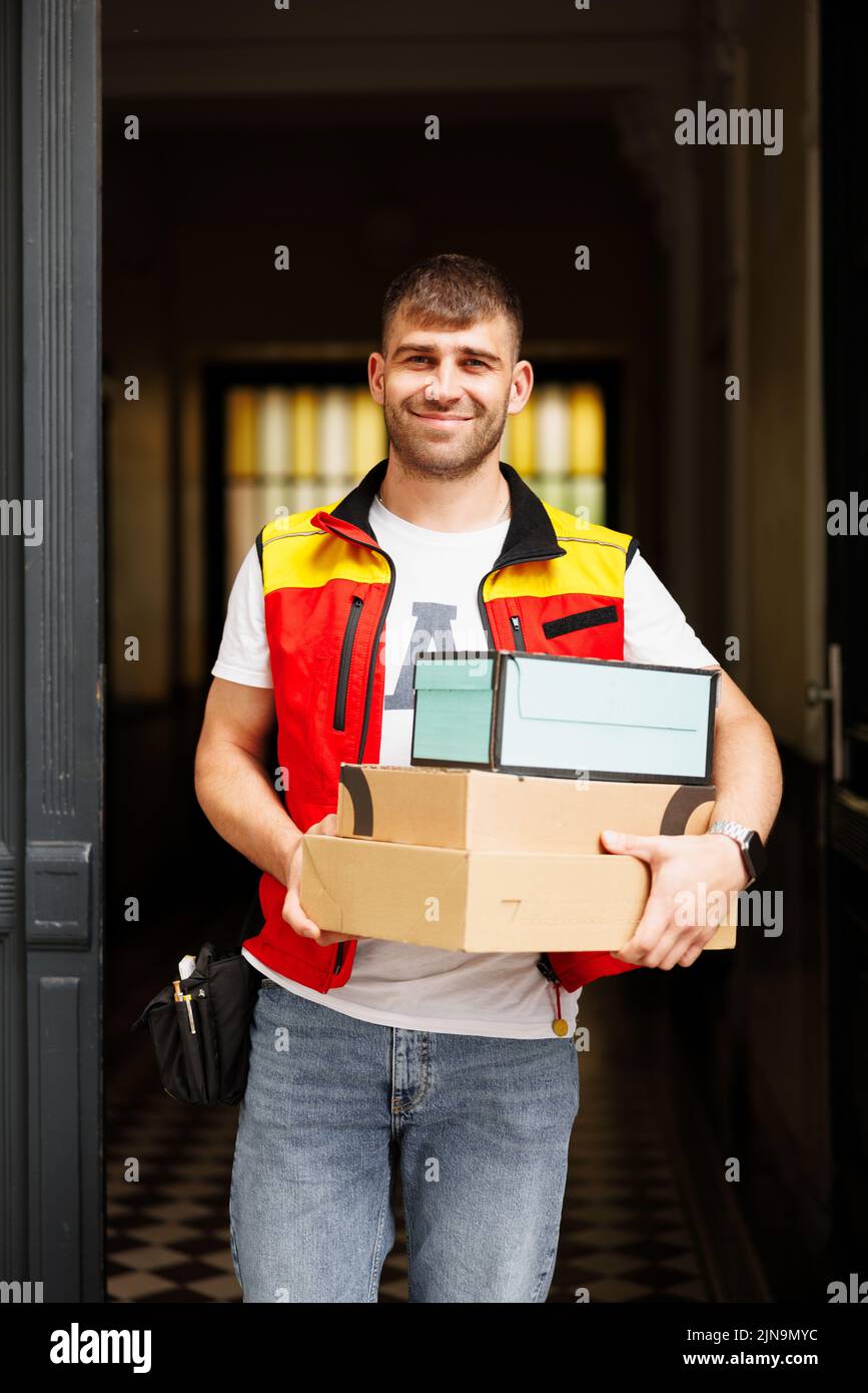 Image of smiling young delivery man standing with parcel box Stock ...