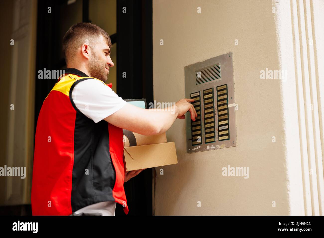 Delivery man pressing button of intercom to enter building Stock Photo ...