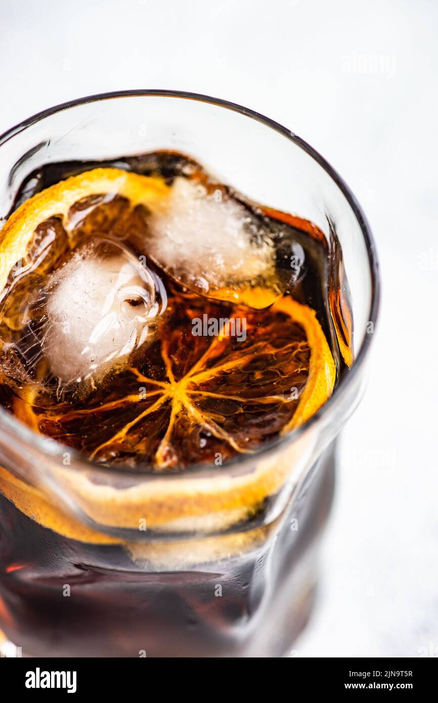 Alcohol cocktail with coke in the glass with orange and ice on grey ...