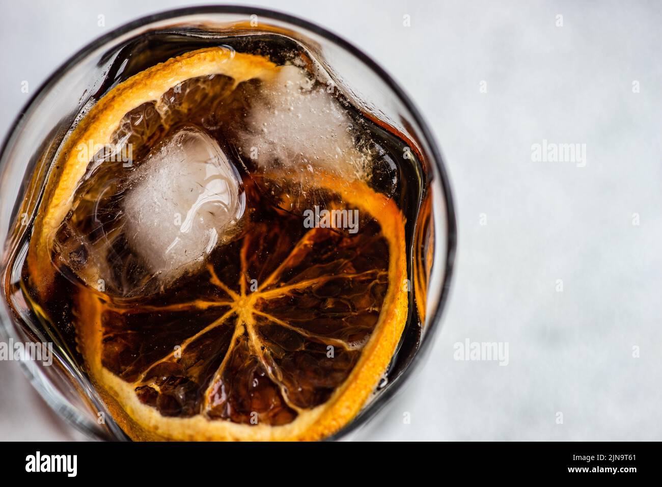 Alcohol cocktail with coke in the glass with orange and ice on grey ...