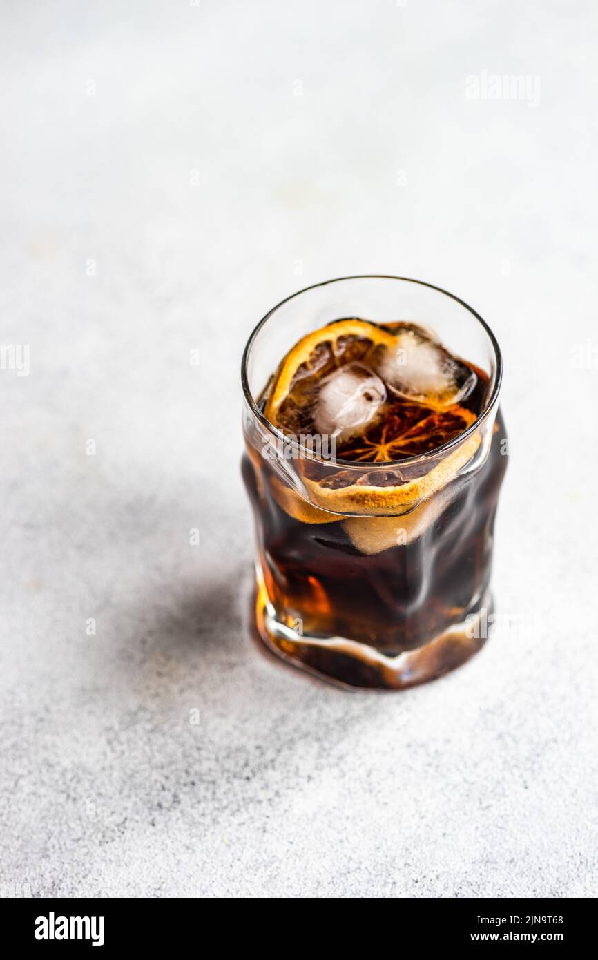 Alcohol cocktail with coke in the glass with orange and ice on grey ...