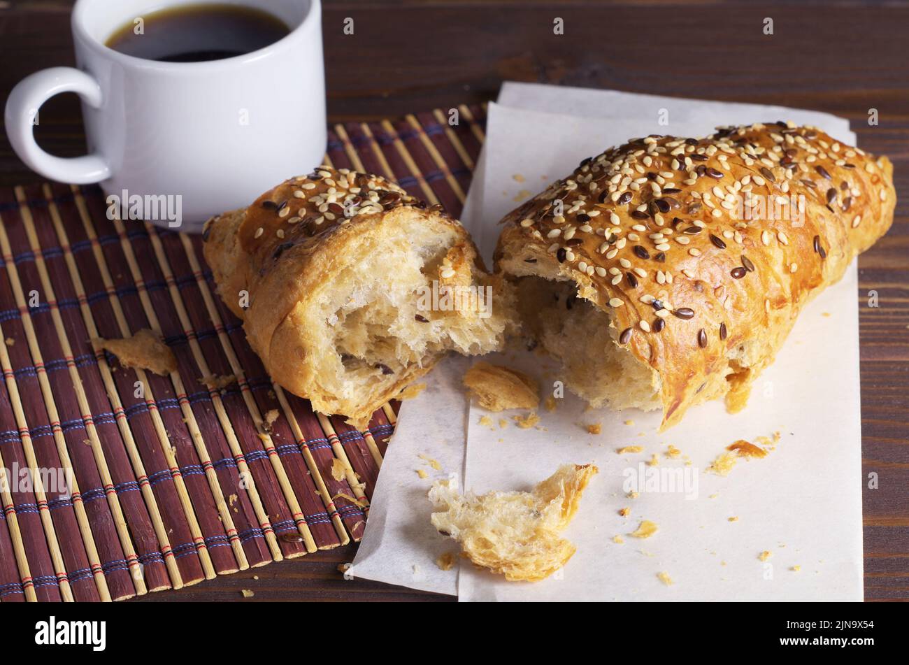 Broken croissant with seeds of flax and cup of black coffee on table ...