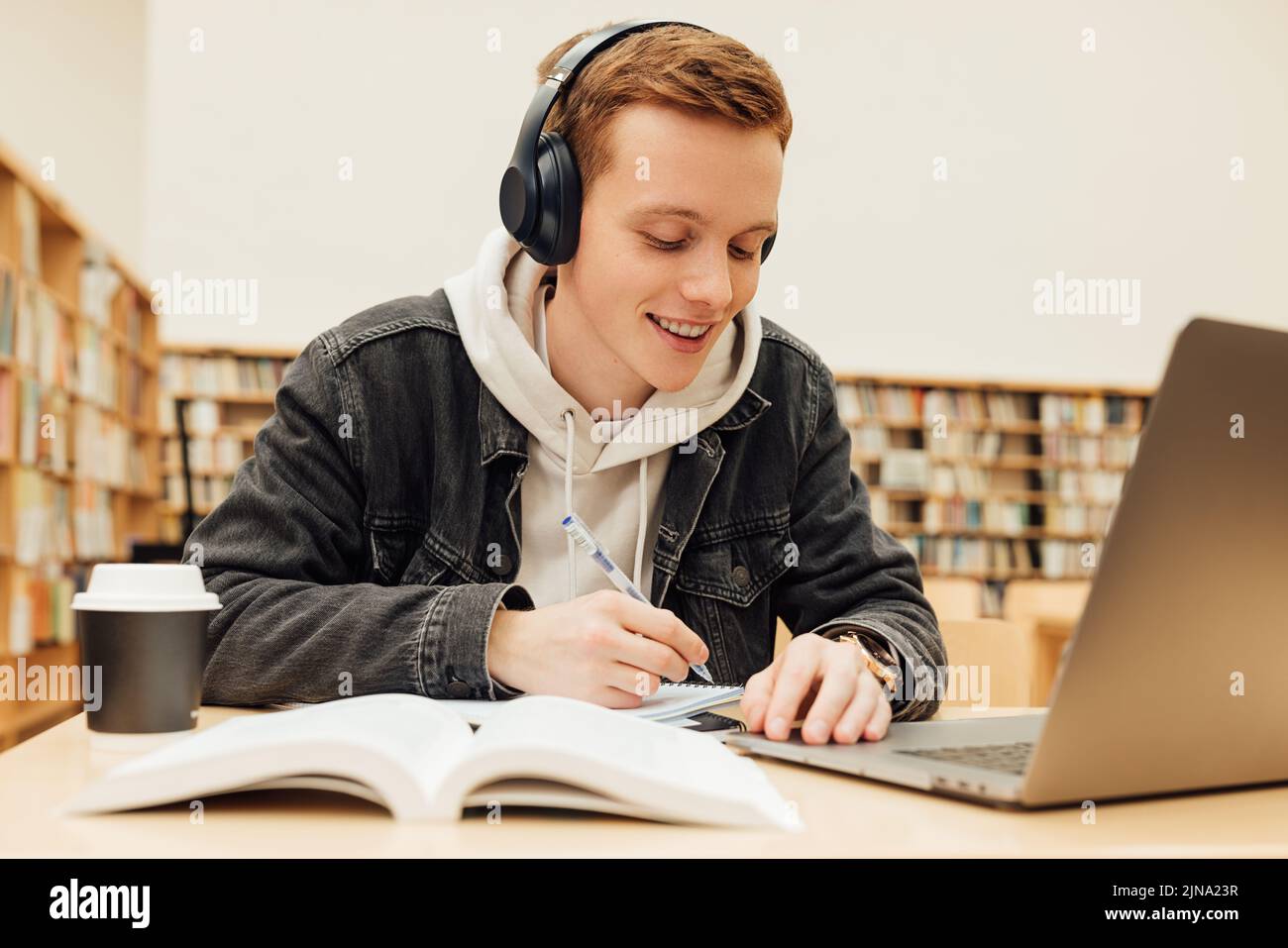 Smiling college student wearing wireless headphones while writing on ...