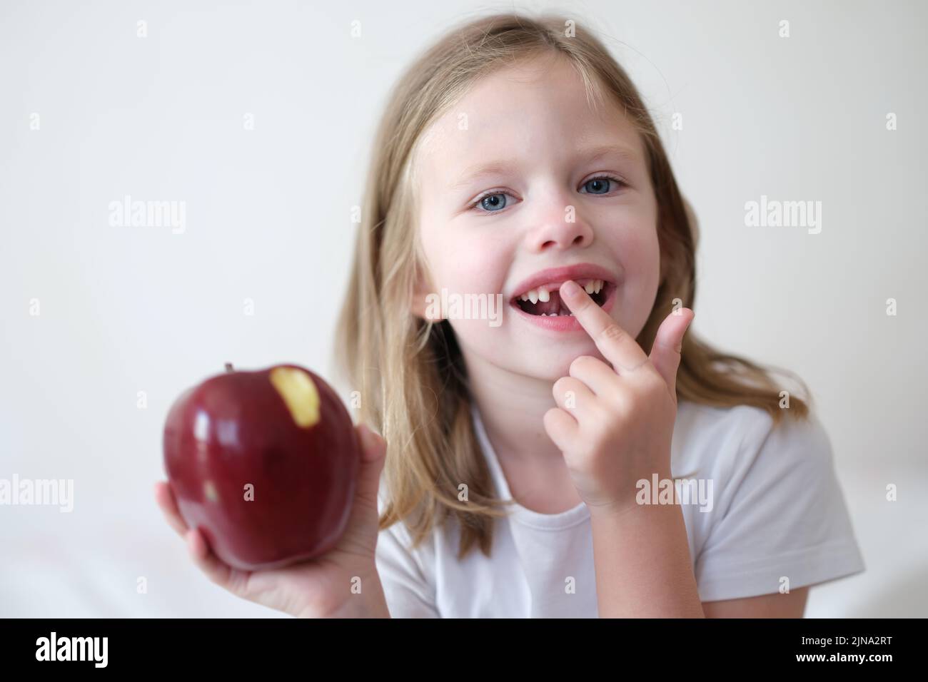 Portrait of smiling cute girl without teeth with red bitten apple in ...