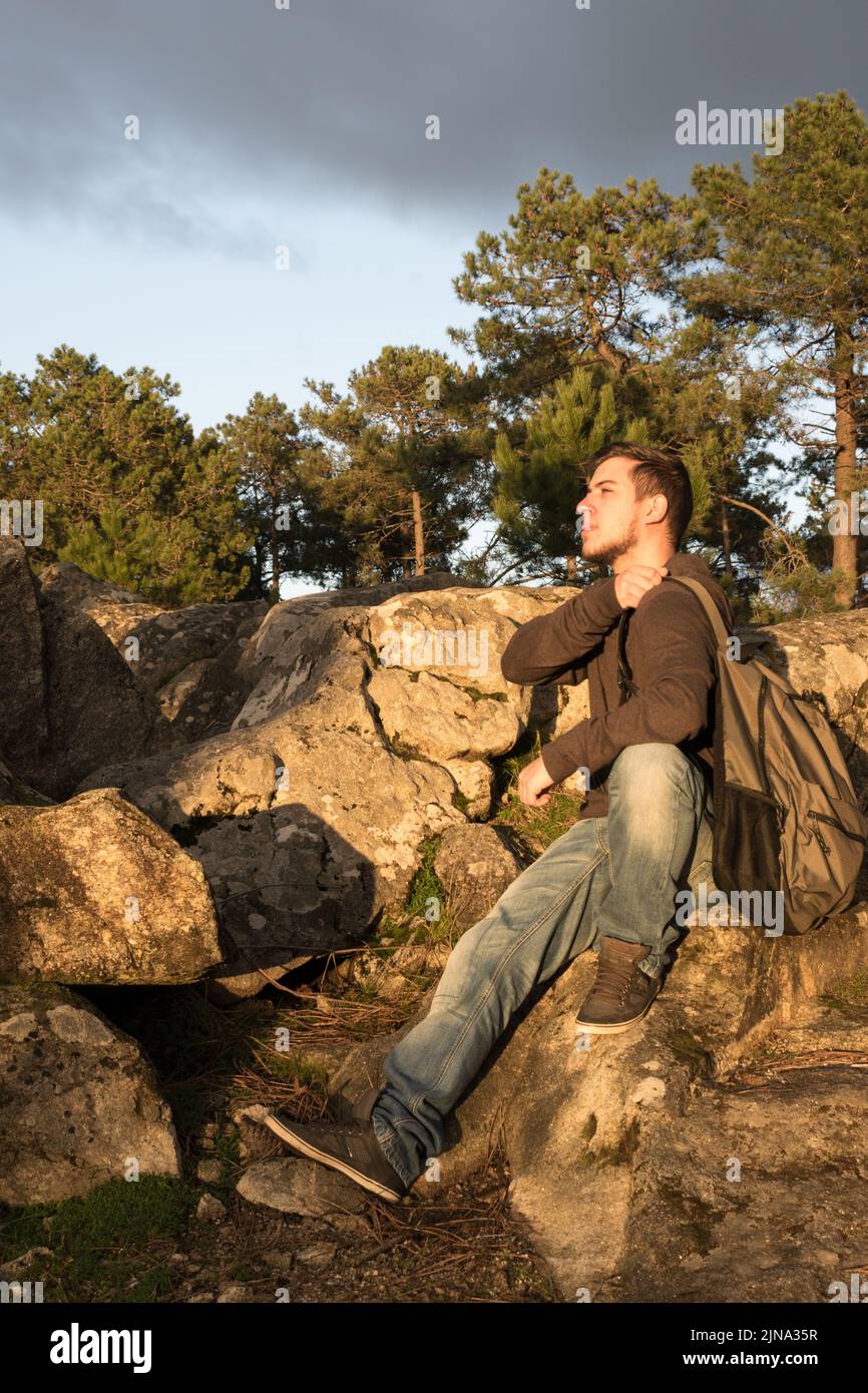 Young boy with a backpack sitting on the rocks in the forest looking at ...