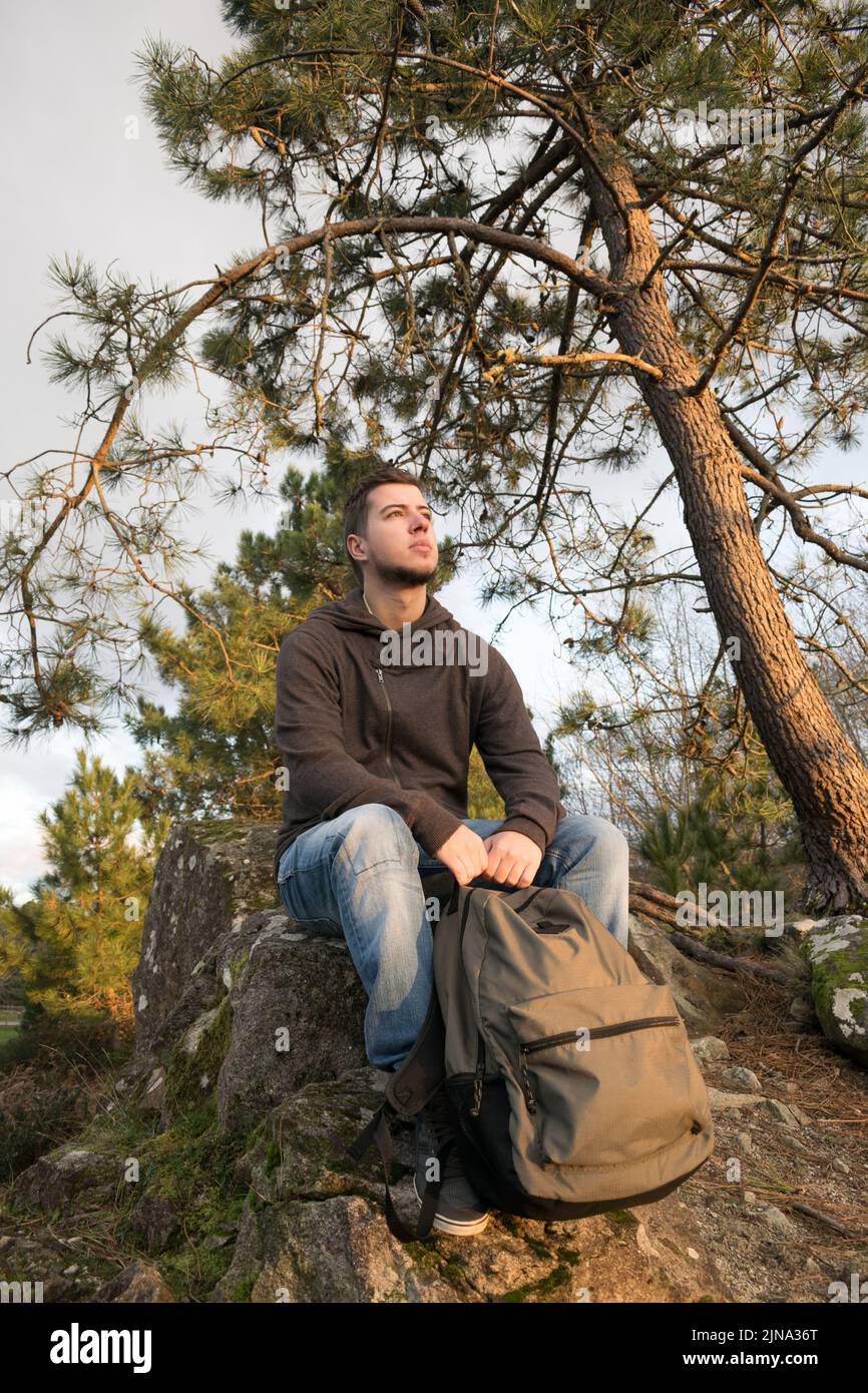 man sitting on a rock with a backpack in the woods looking at the ...