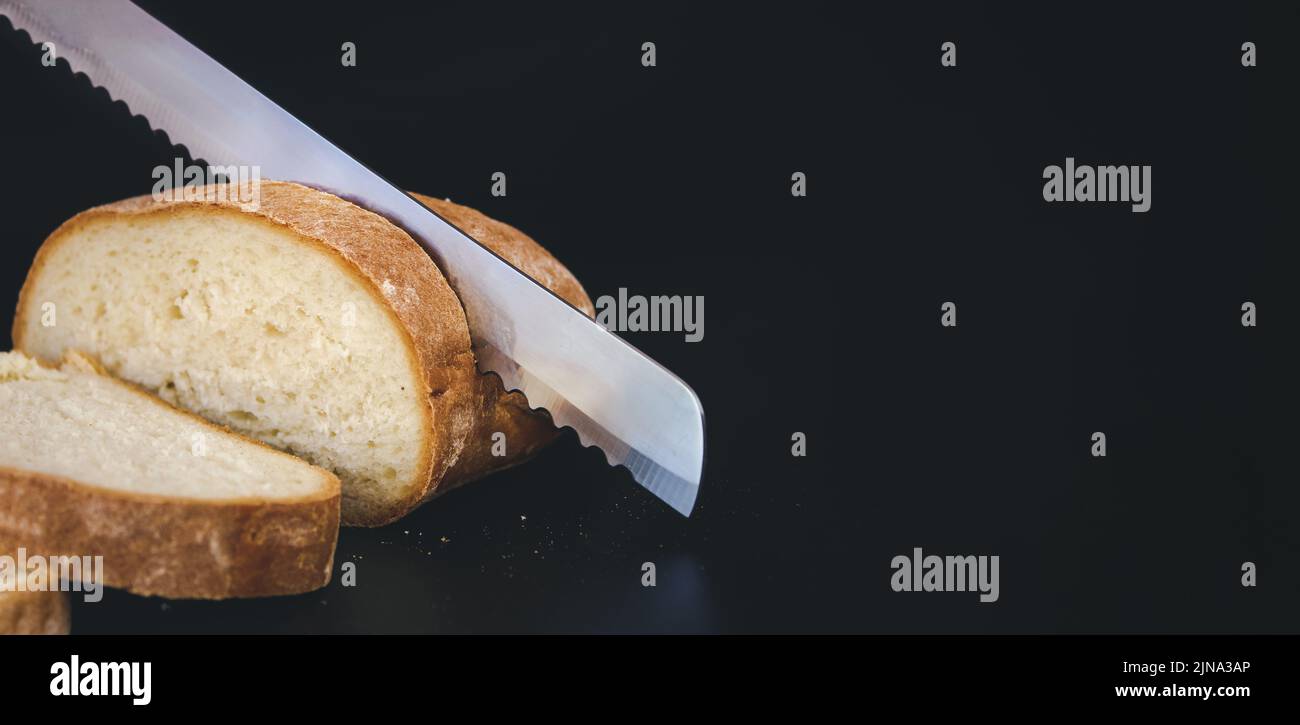 A large knife cuts thin pieces of white bread from a rectangular loaf ...