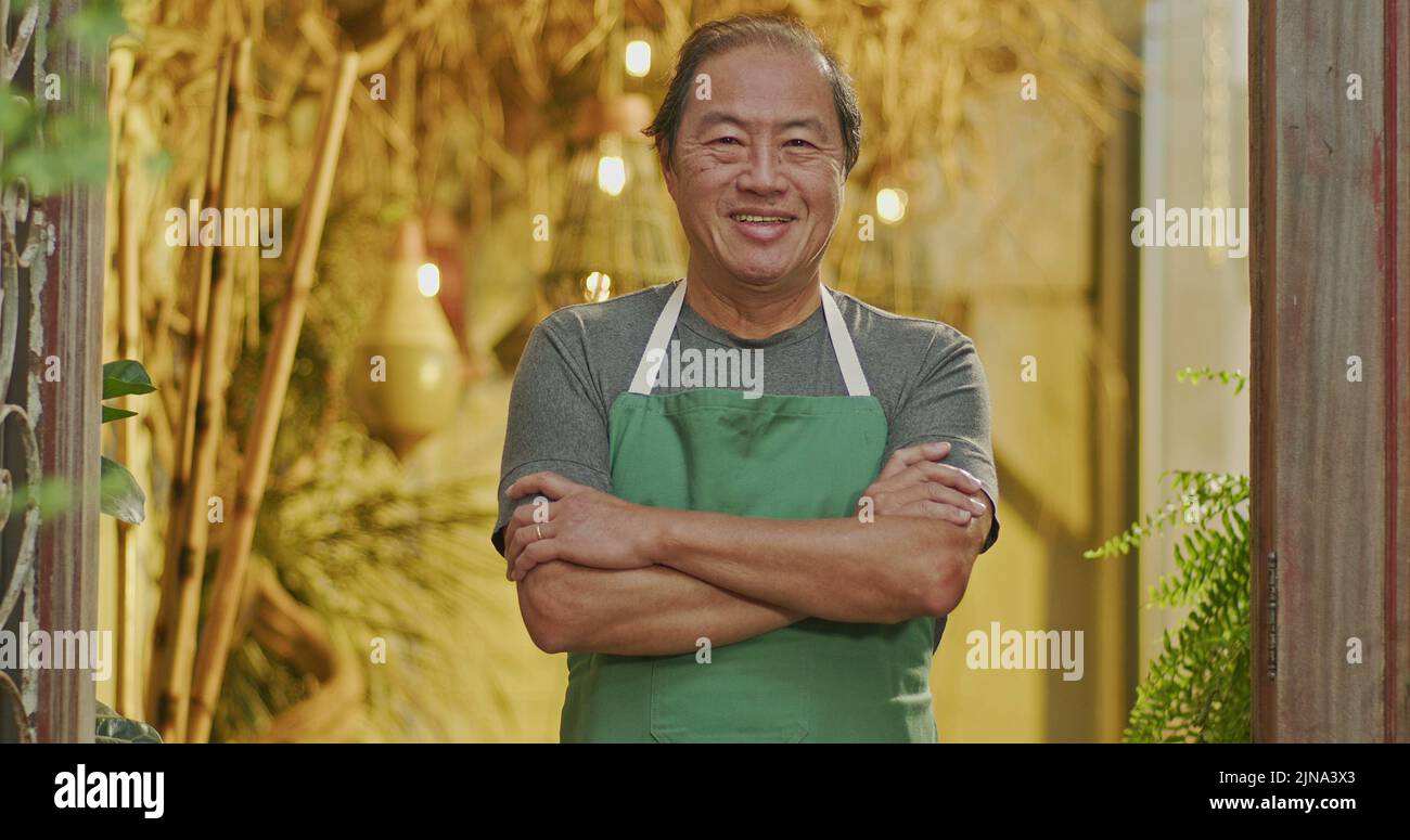 An Asian American business owner wearing apron and crossing arms ...