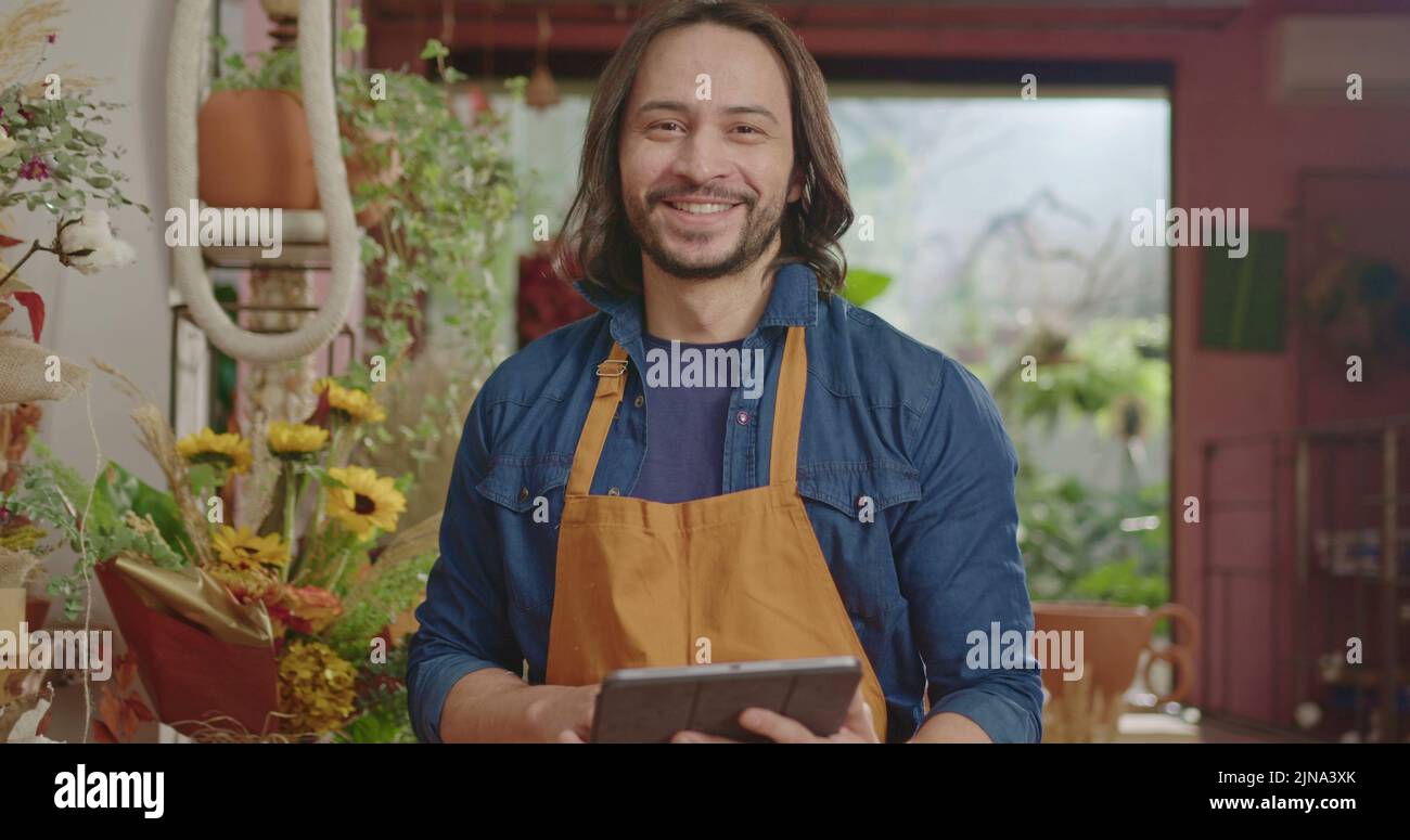 Portrait of a male worker wearing apron and holding tablet turns head ...