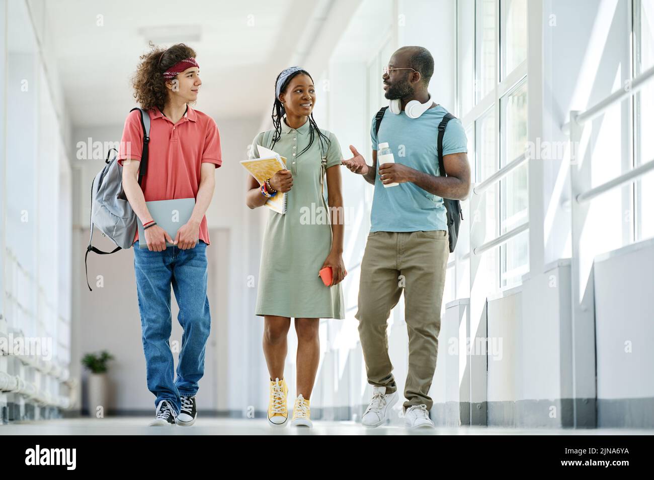 Multiethnic friends talking to each other while walking along school ...