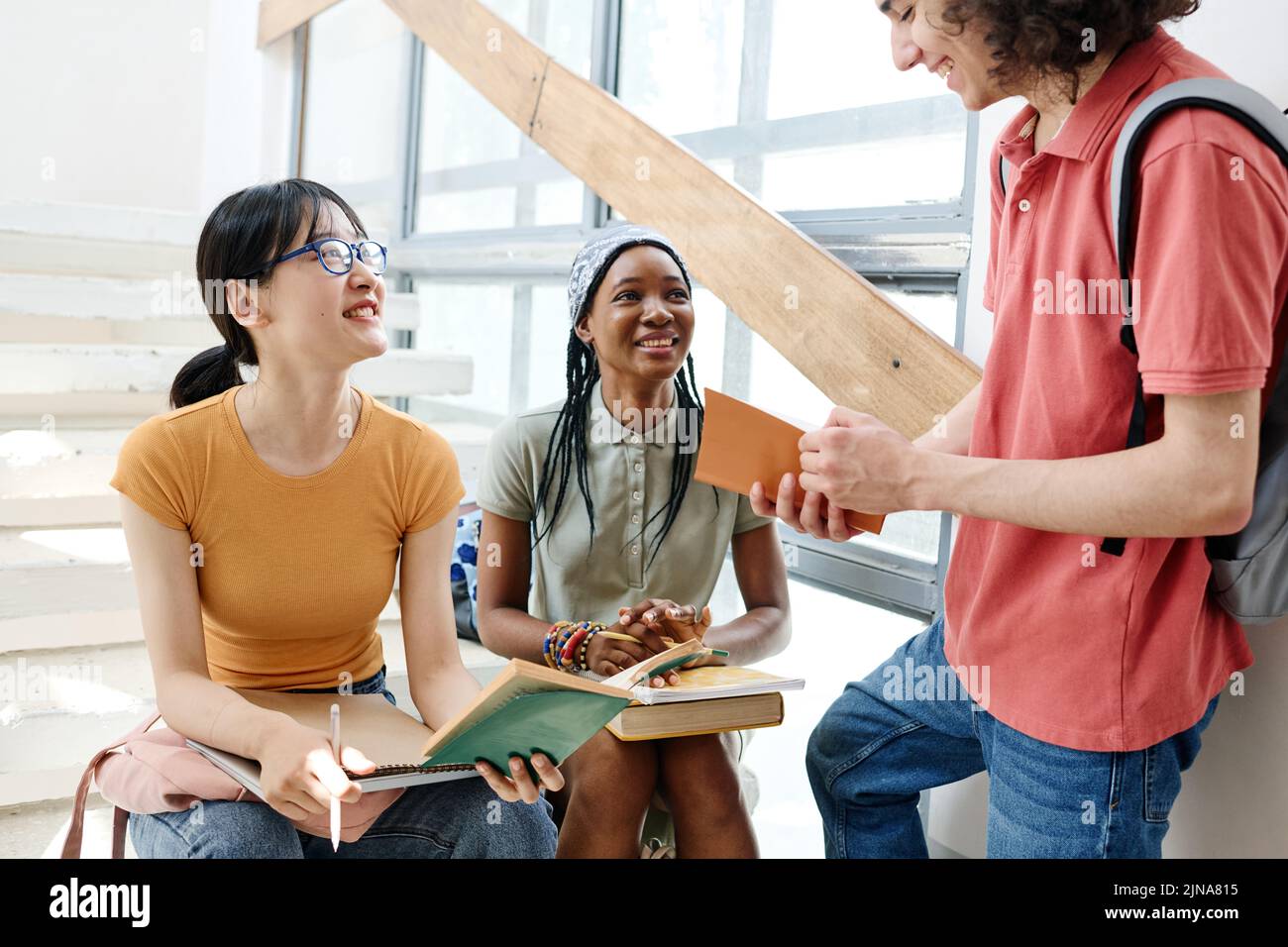 Group of teenagers reading textbooks and talking to each other, they ...