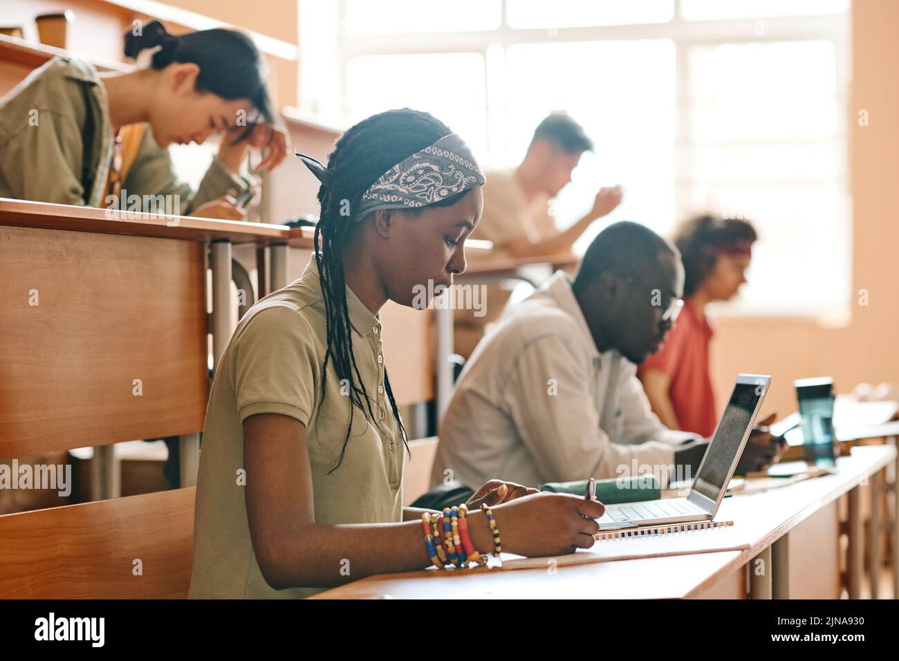 Group of students sitting at desk with laptop and books and writing ...
