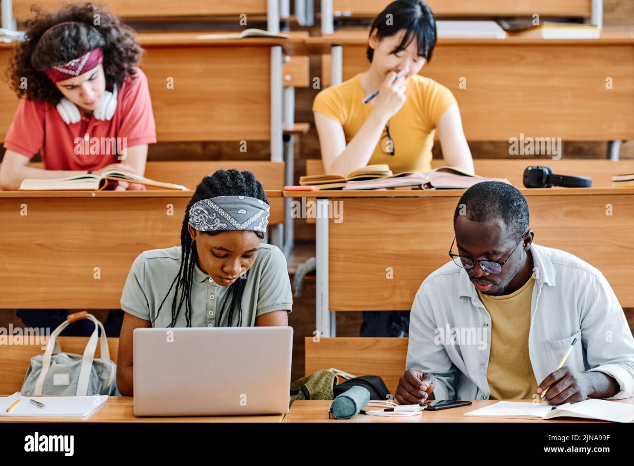 Group of students sitting at desks and writing exam at auditorium of ...