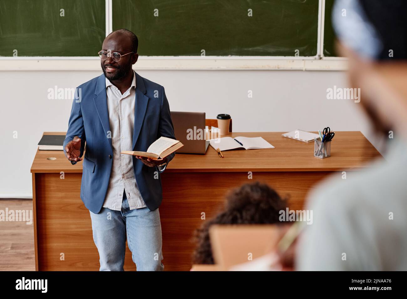 African teacher standing with book and reading lecture for students at ...