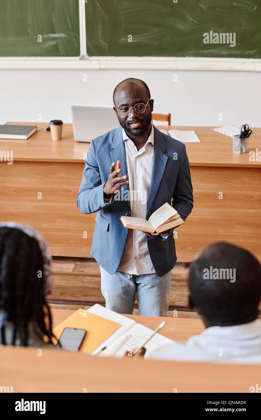 African teacher with book telling lecture to students standing at ...