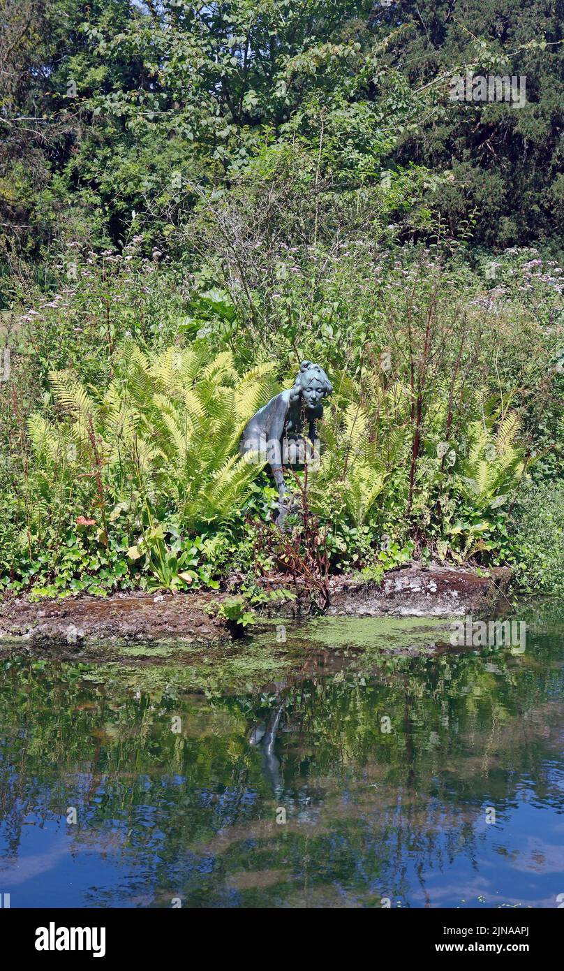 Water nymph statue, looking at reflecion in ornamental pond. Amongst ...