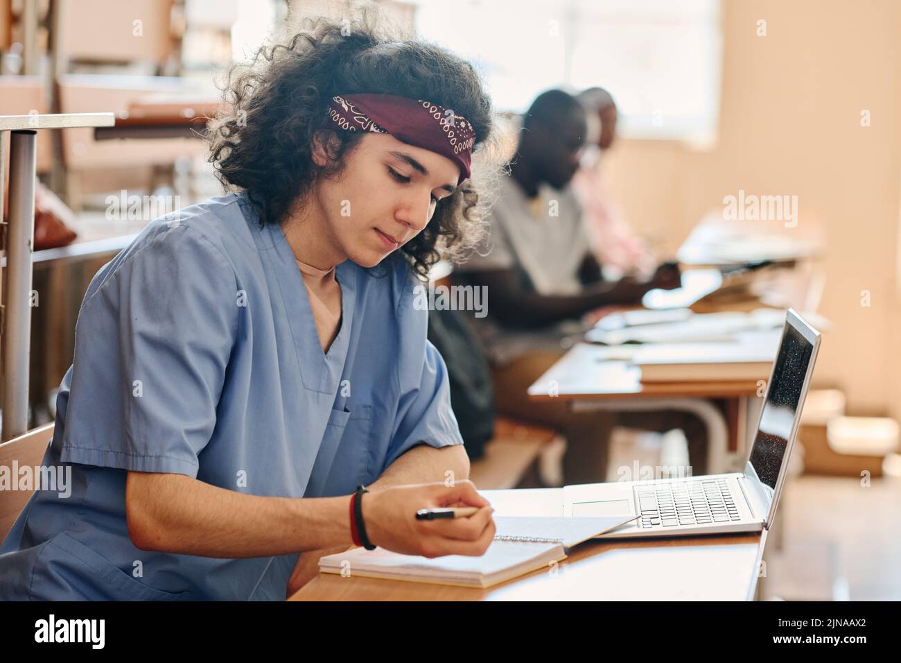 Serious medical student in uniform sitting at desk with copybook and ...