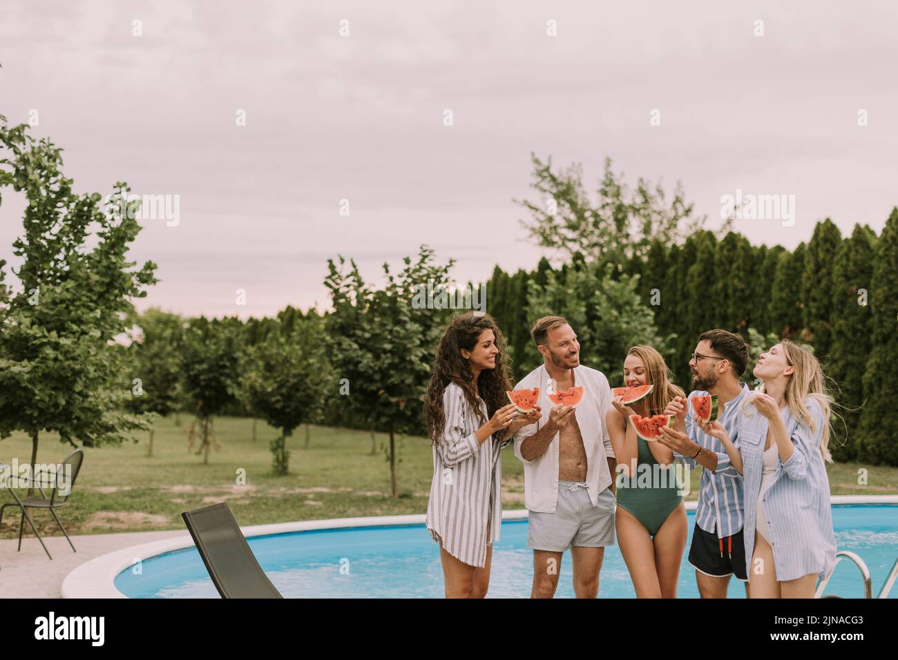 Group of young people standing by the swimming pool and eating ...