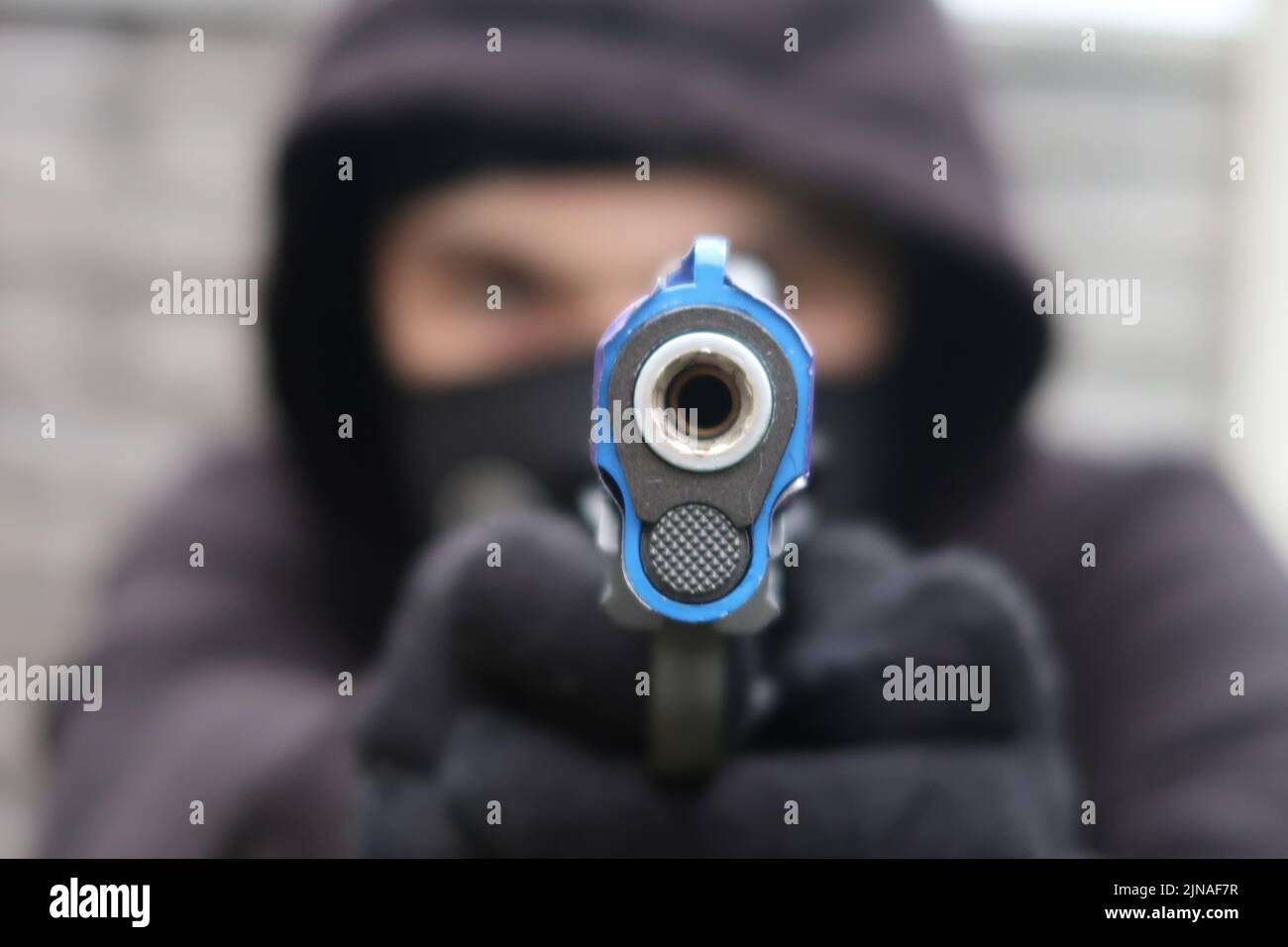 A pointing gun in the hands of a masked man with black clothes and ...