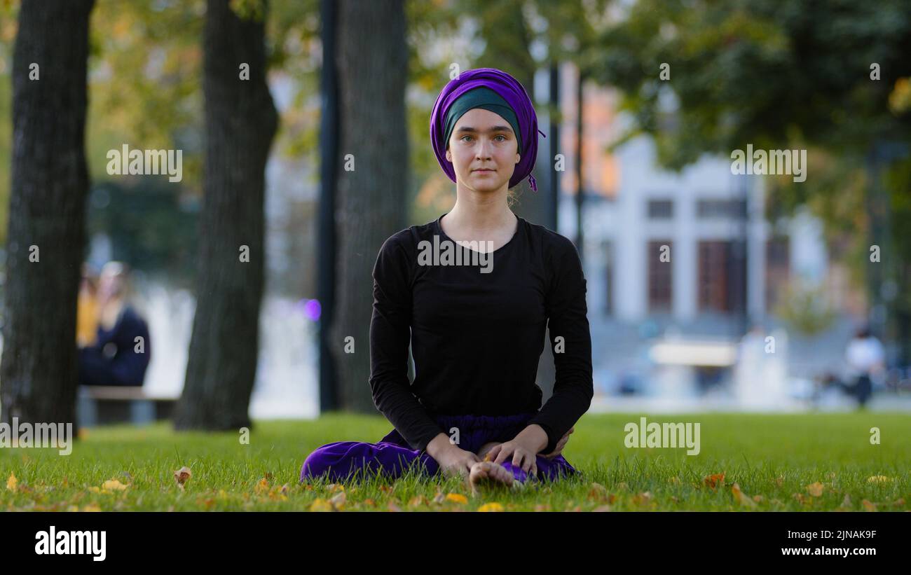 Young girl muslim woman in hijab sits on green grass in park takes leg ...