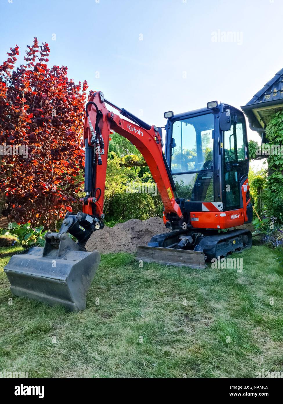 A small red Kubota excavator in a green garden Stock Photo - Alamy