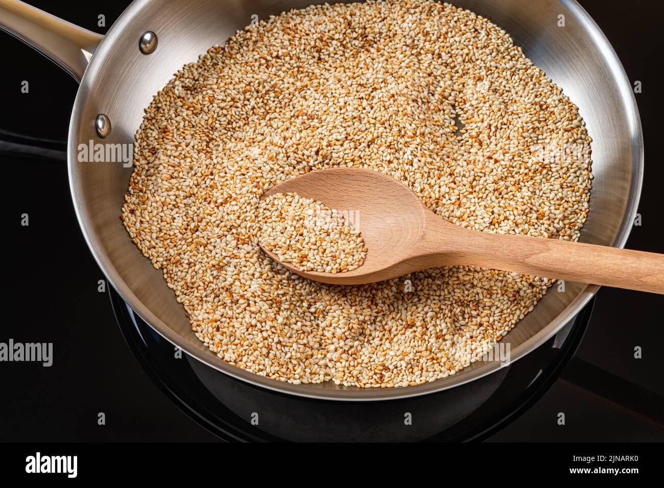 Sesame seeds toasting in a stainless steel frying pan. Roasting white ...