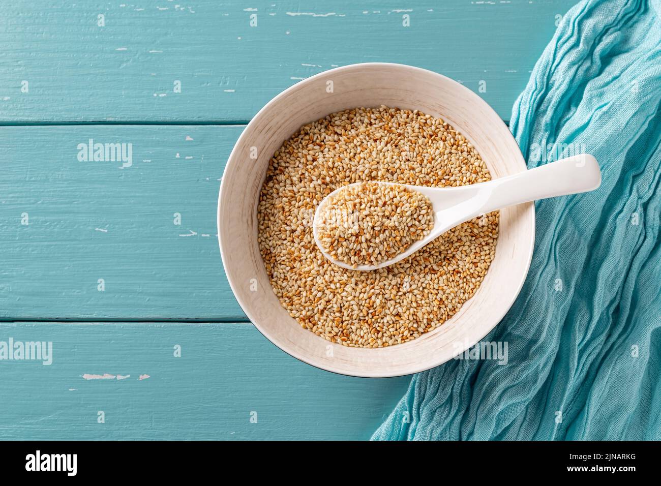 Toasted sesame seeds and white spoon in a bowl over teal wooden ...