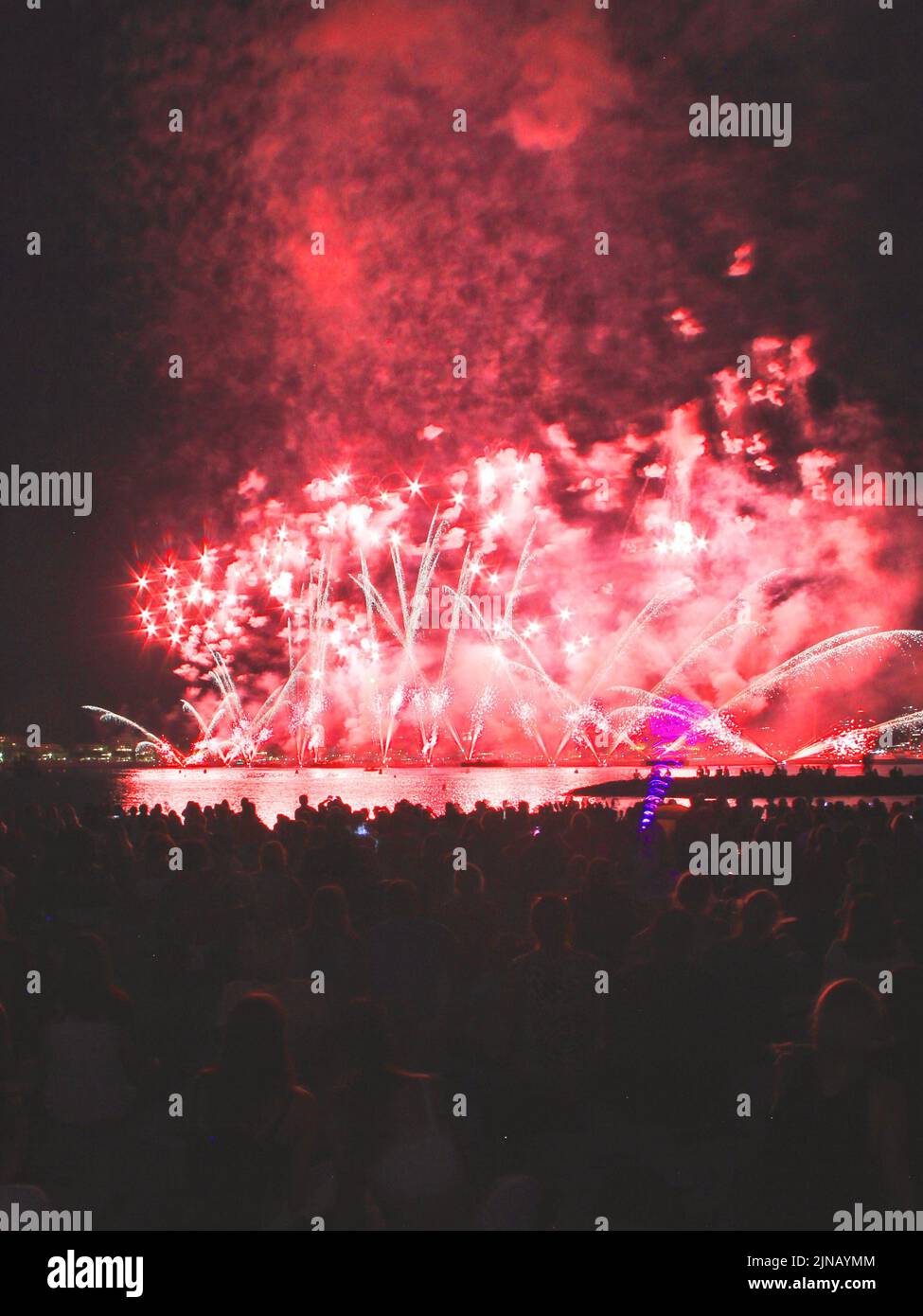 Red fireworks exploding ina smoky evening on the sea with people ...