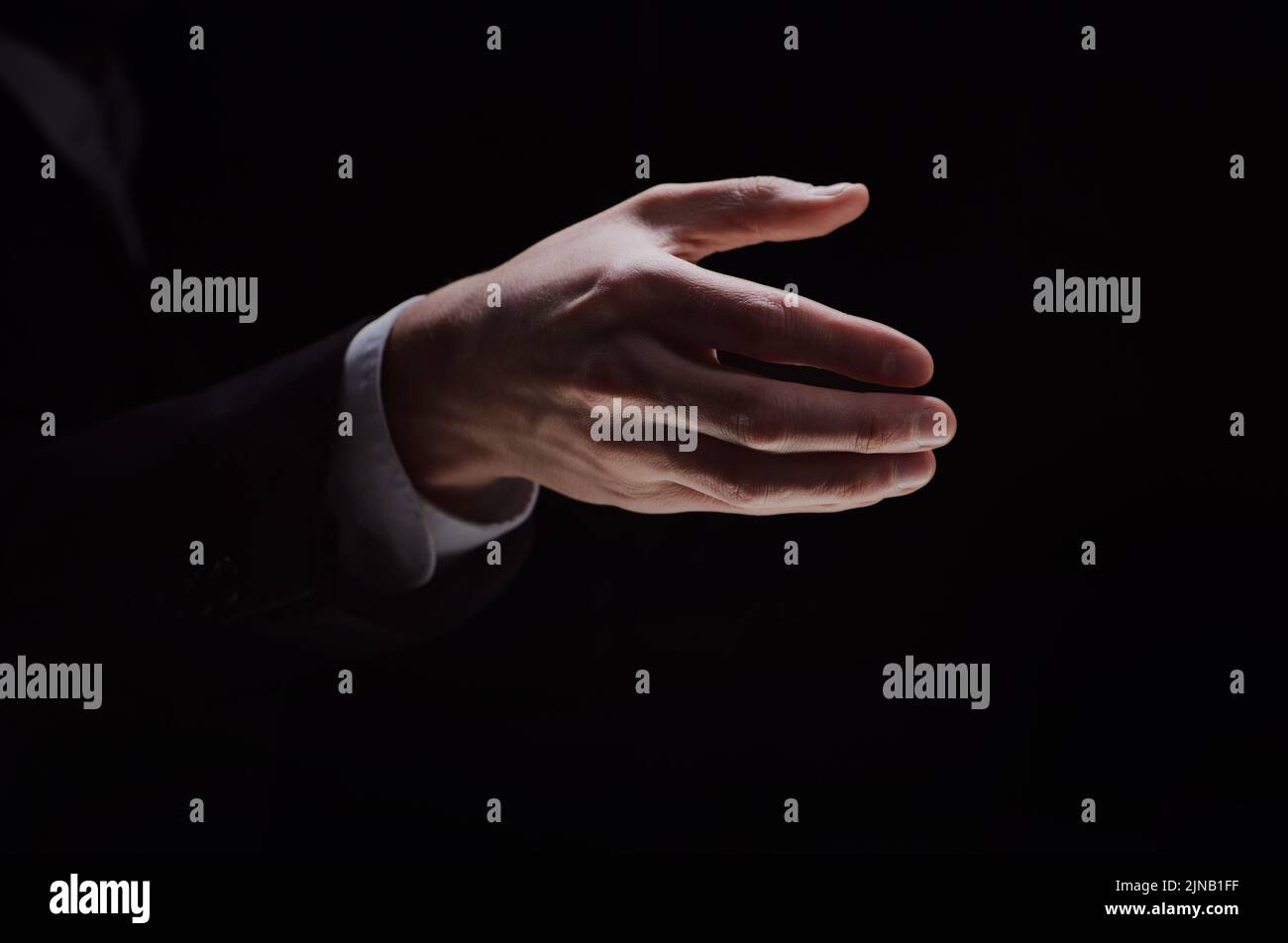 A man holds out his hand for a handshake, highlighted on a black ...